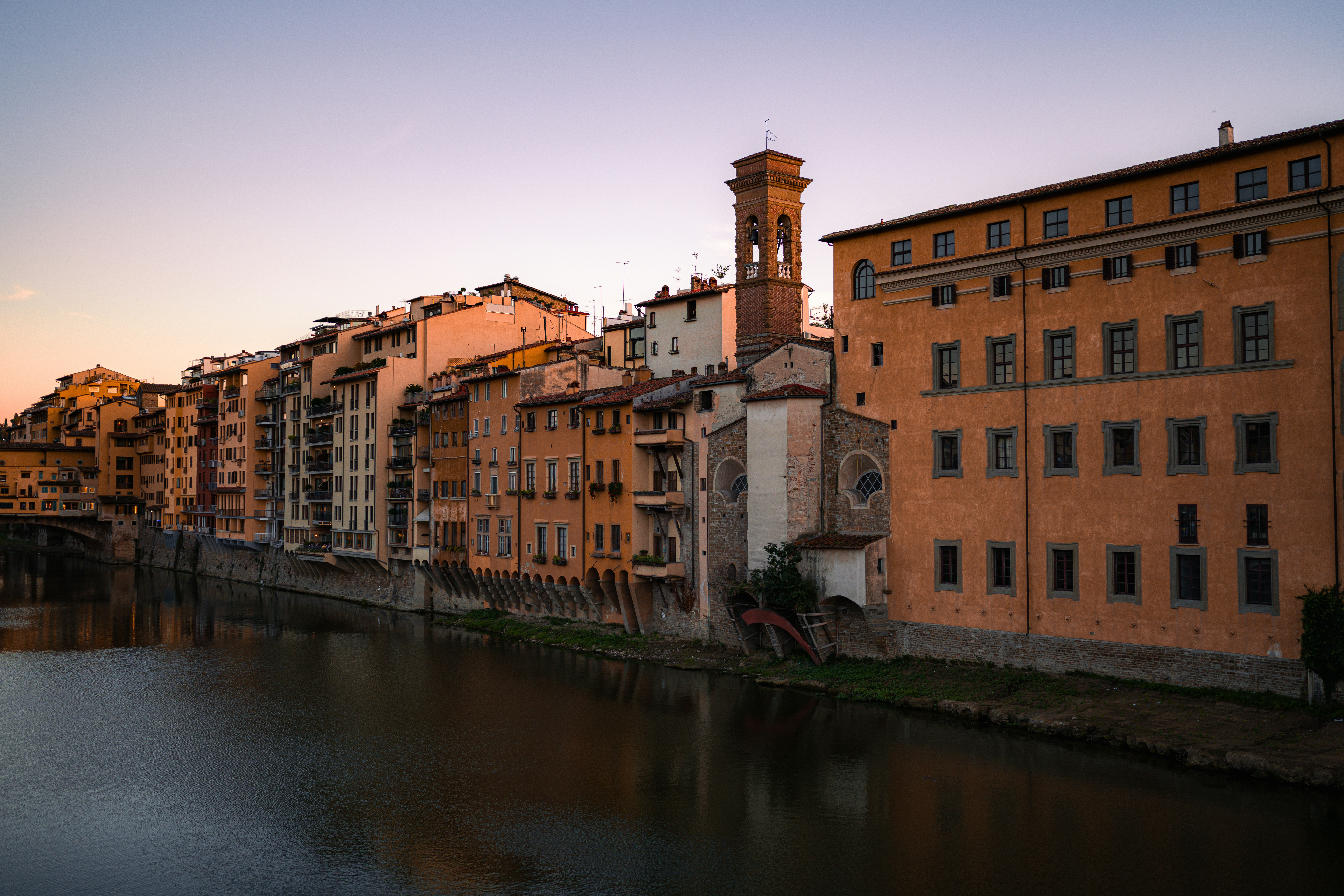 Buildings line a river at sunset with warm light.