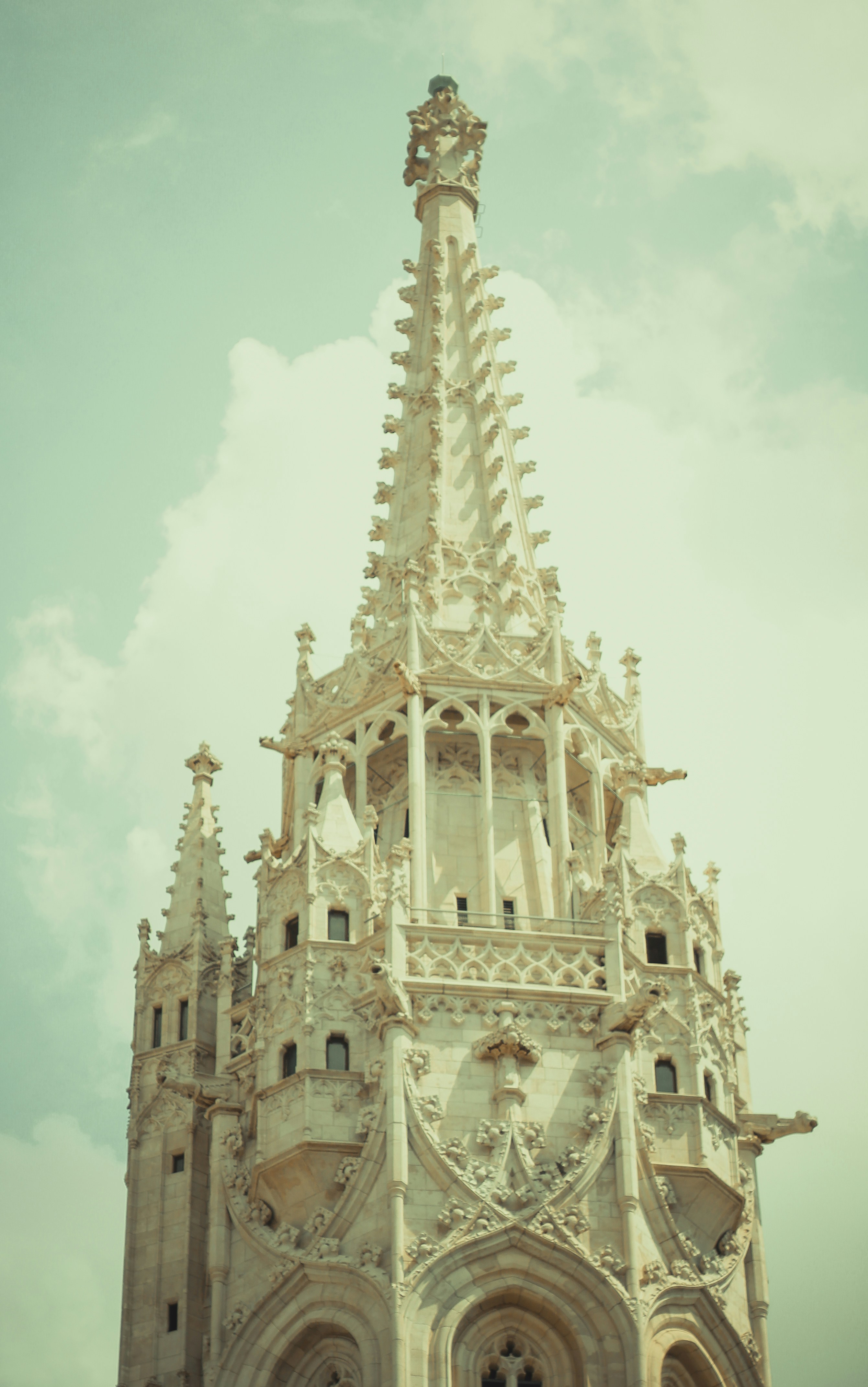 Intricate Gothic tower adorned with detailed carvings and spires, reaching towards a cloudy sky.