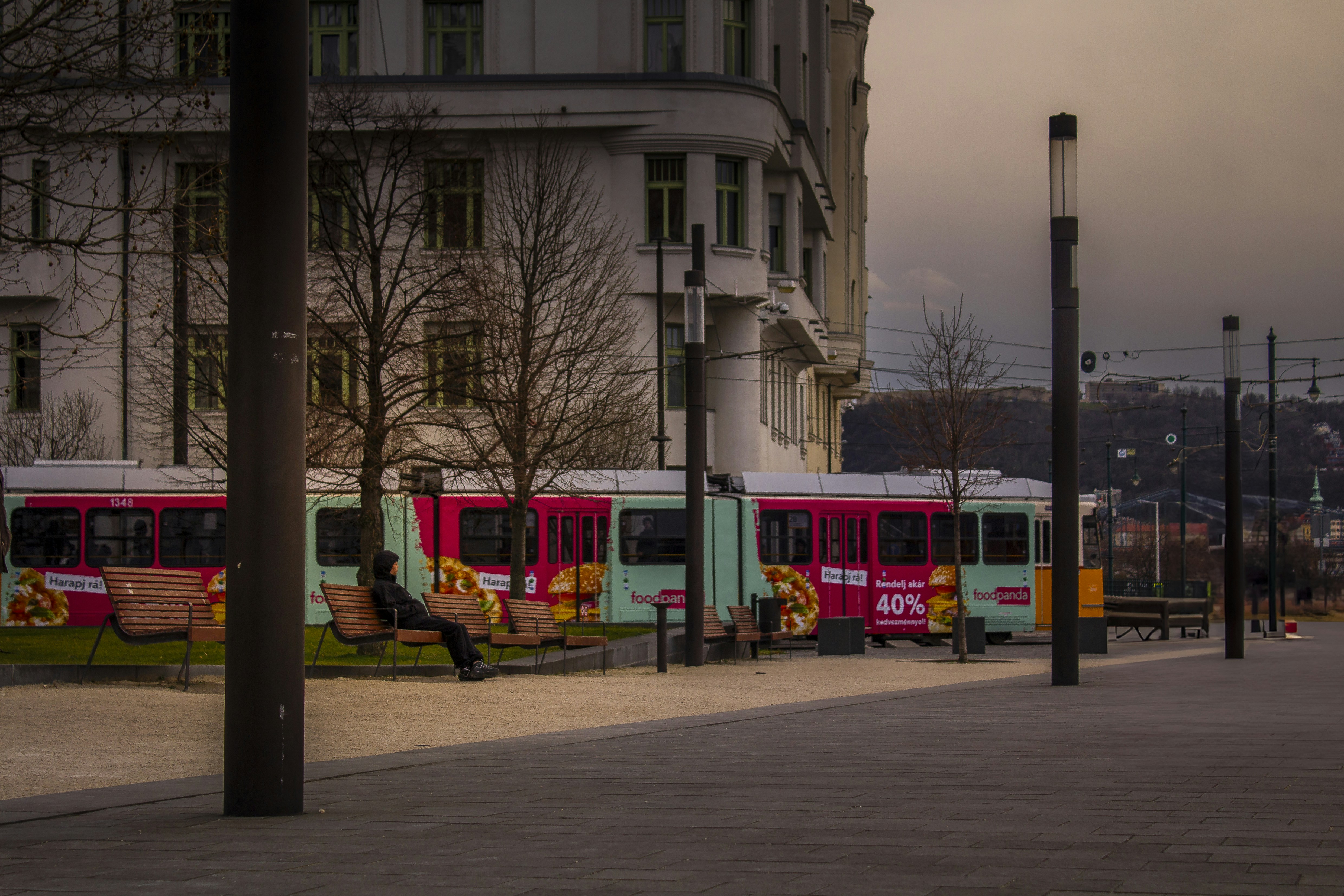 A person sits on a bench near a colorful tram.
