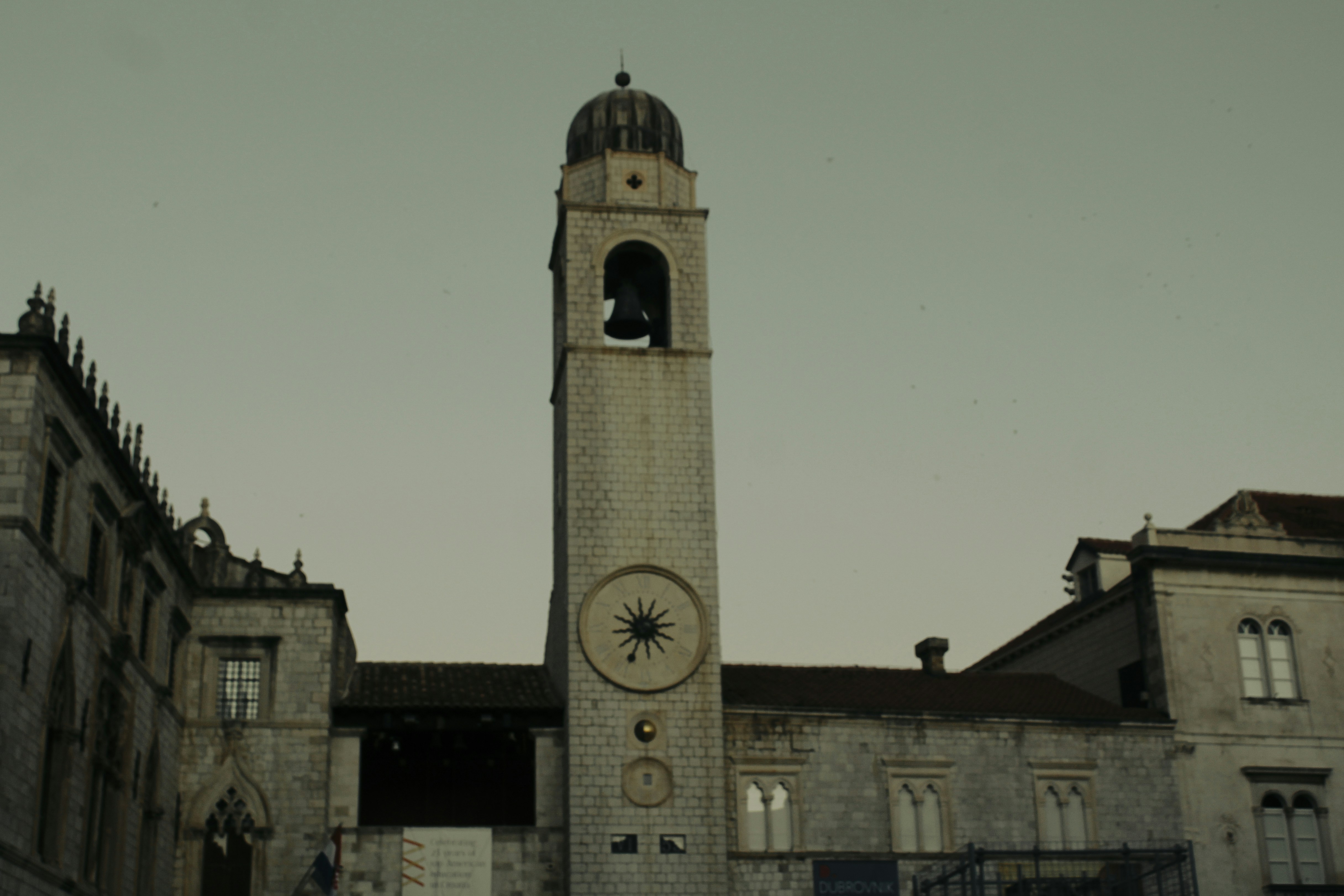Historic clock tower stands tall against a muted sky, showcasing intricate architectural details and a prominent sun dial.