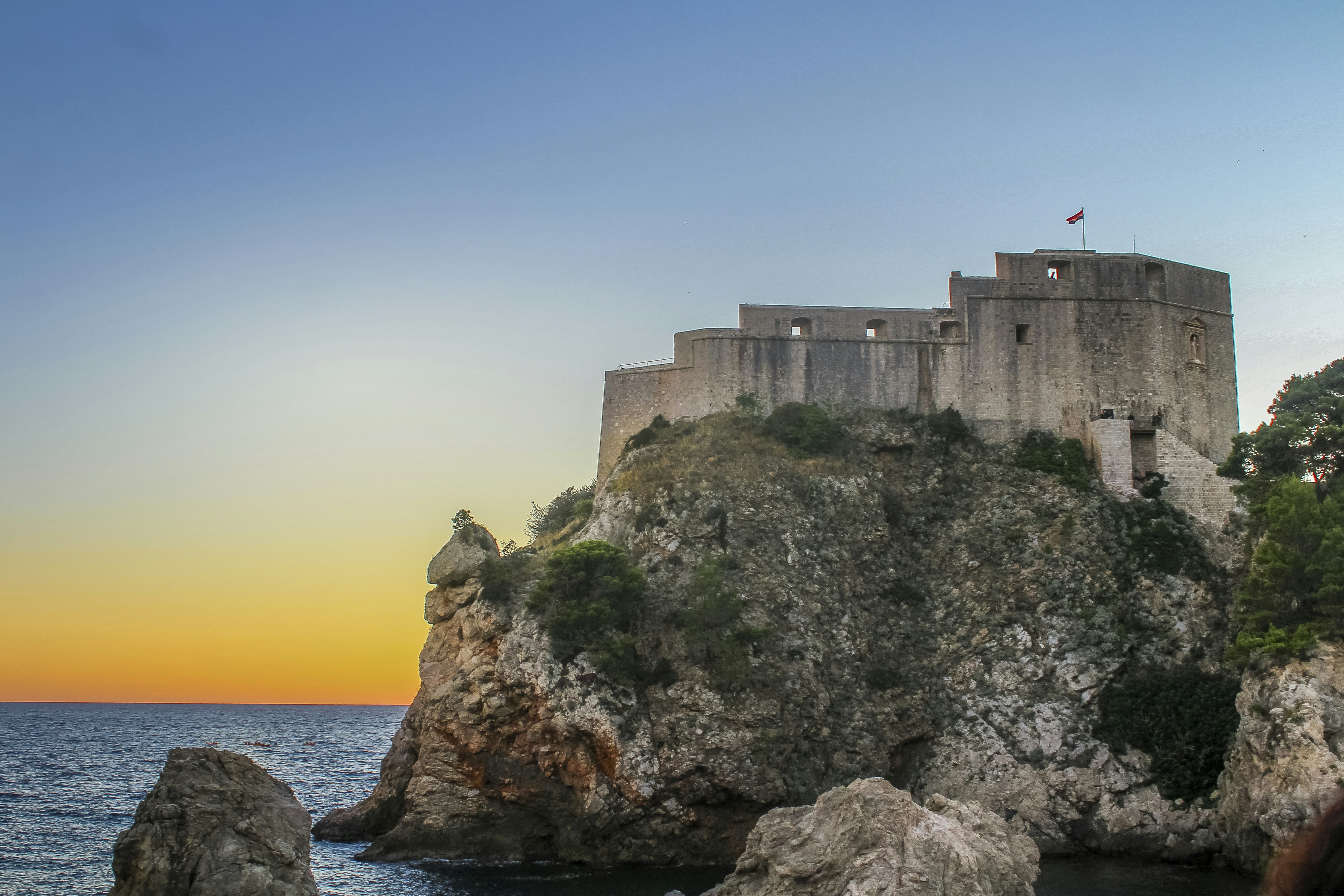 Ancient fortress perched on a rocky cliff overlooking the tranquil sea at sunset.