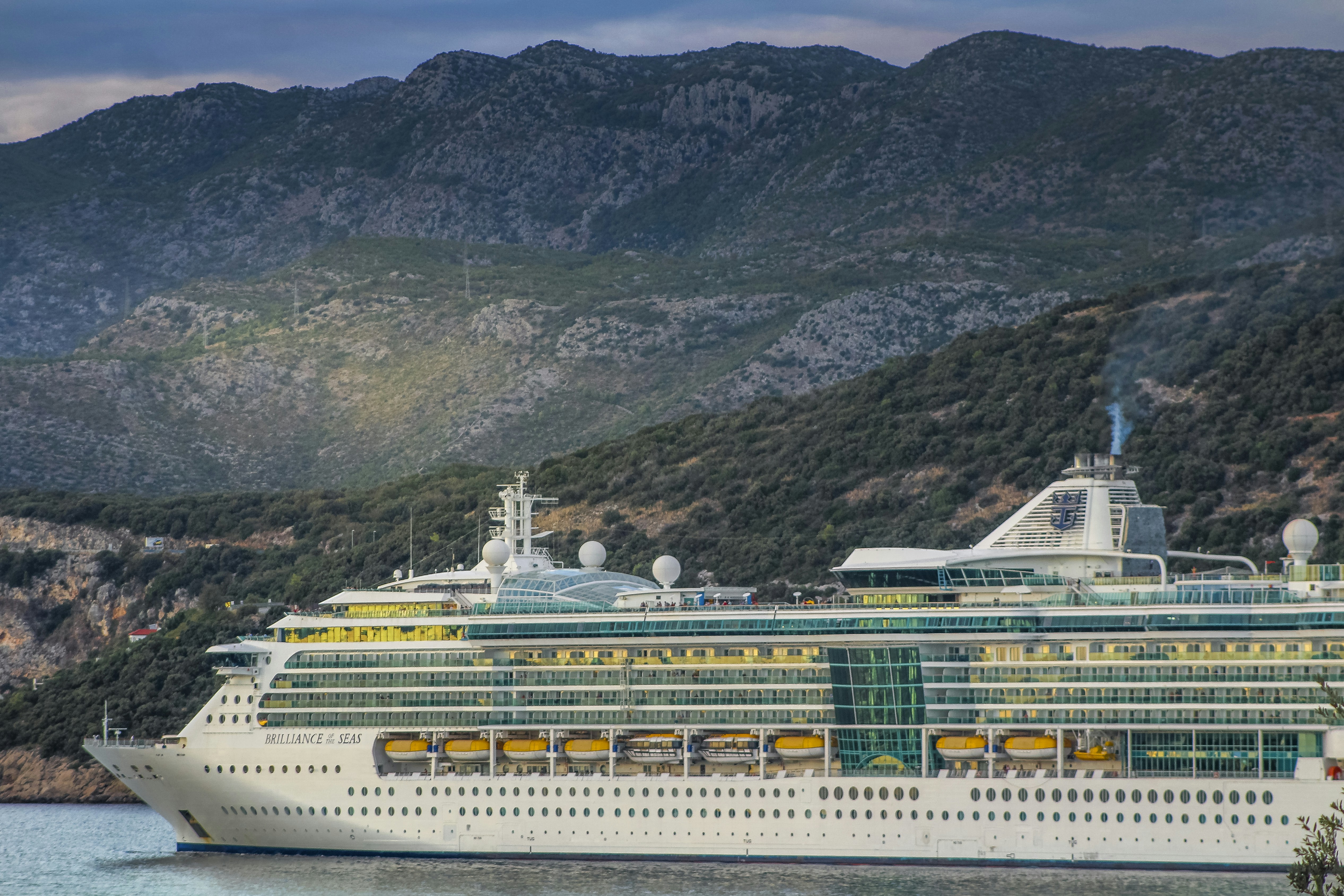 A large cruise ship sails near a mountainous coastline.