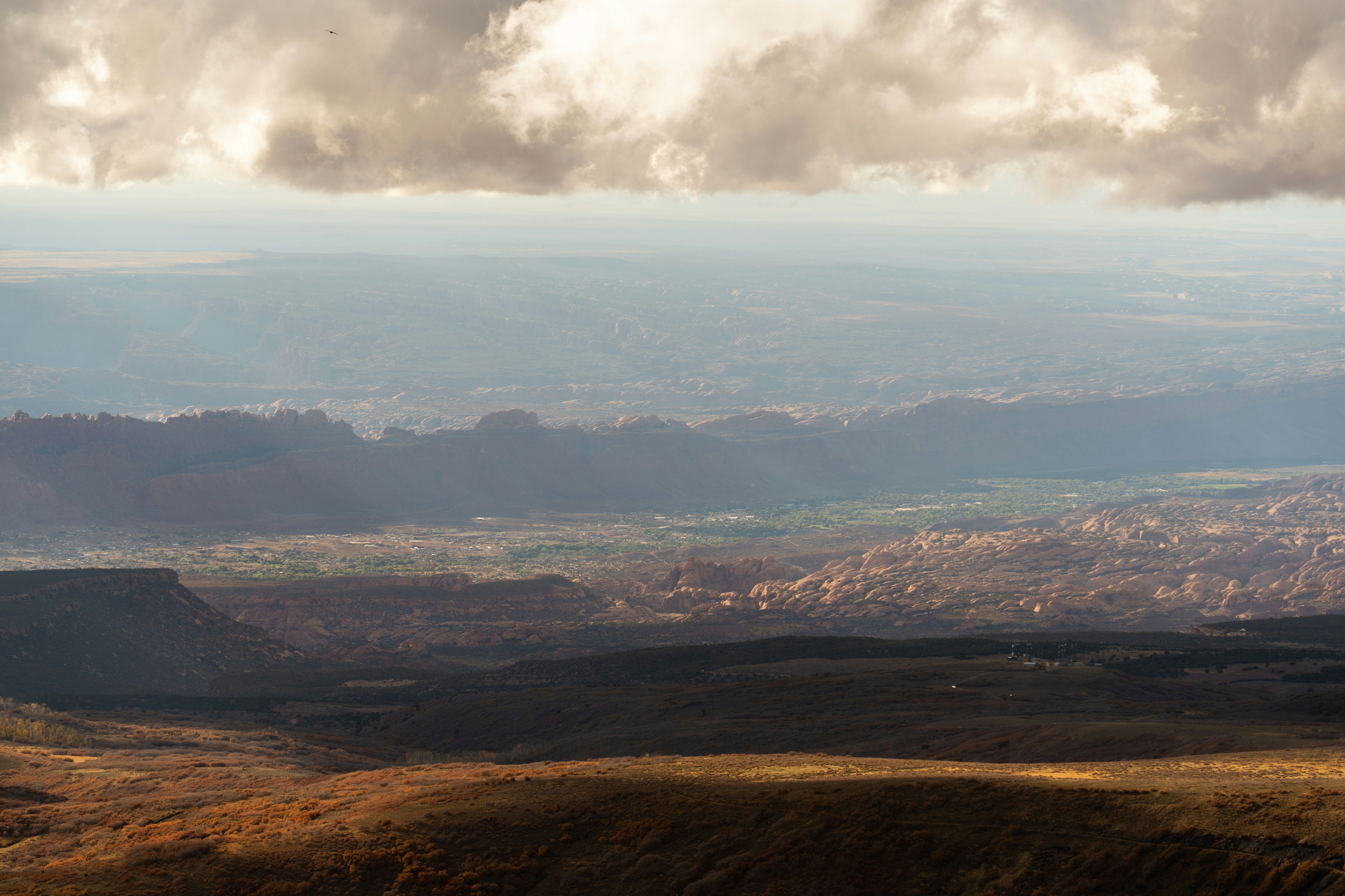Dramatic landscape showcasing layered hills and valleys under a cloudy sky, with sunlight breaking through the clouds. The scene evokes a sense of depth and tranquility.