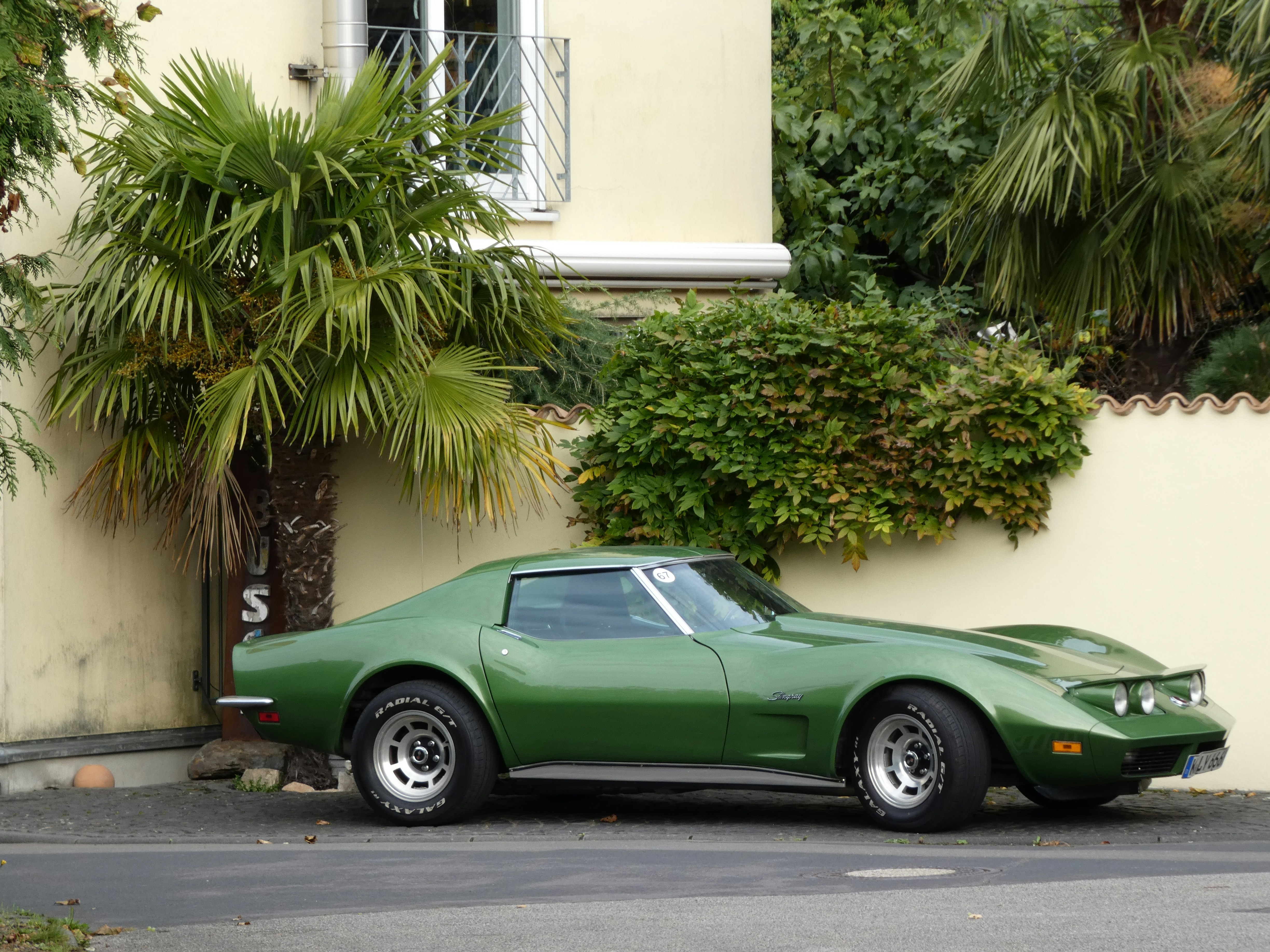 Zielona Corvette. Znajdź domenę która przyspieszy Twój biznes. | Green vintage car parked near palm trees and building