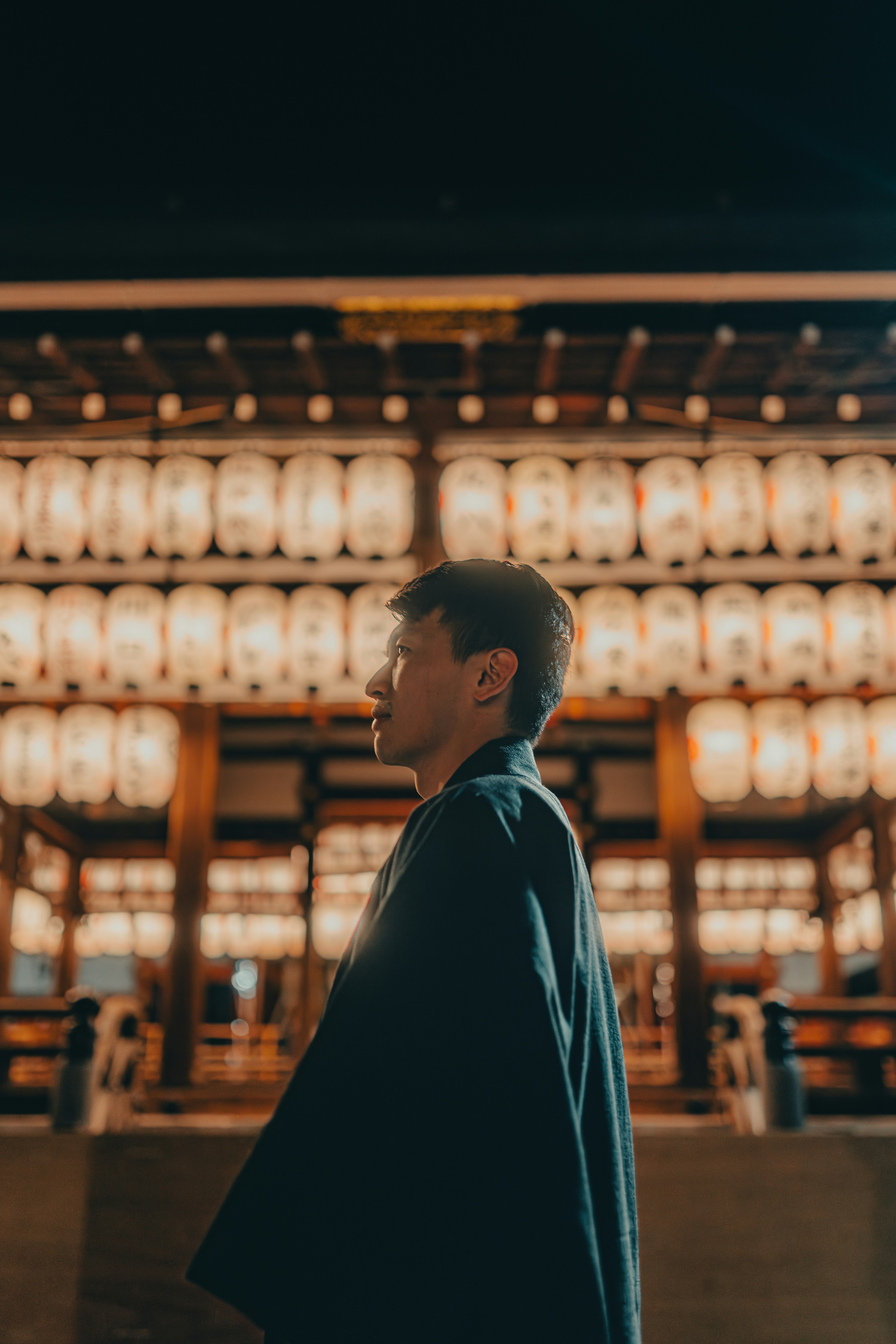 A man in traditional attire stands in profile against a backdrop of glowing lanterns, embodying a tranquil moment amidst vibrant cultural illumination.