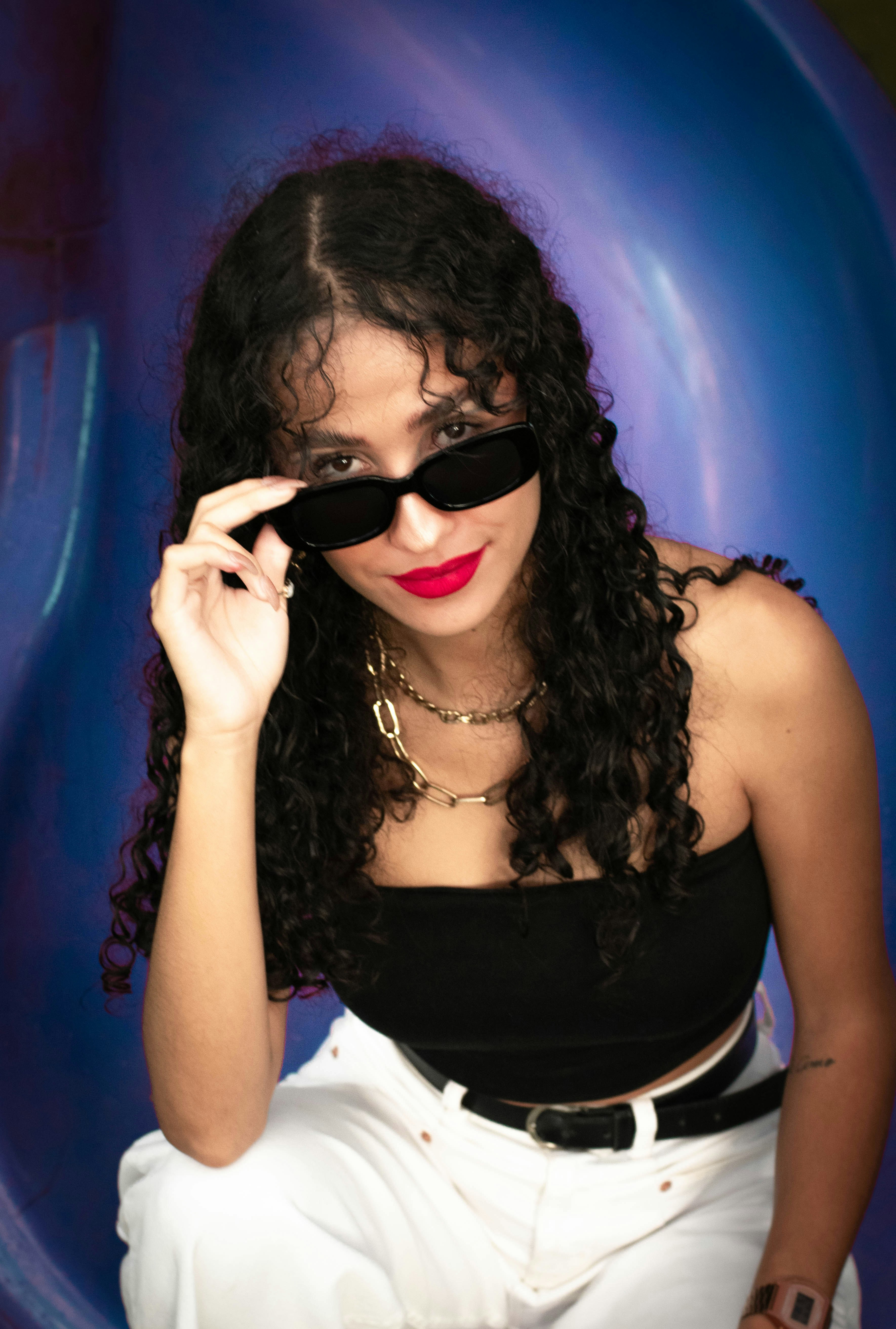 Young woman in stylish attire and sunglasses poses confidently against a vibrant background.