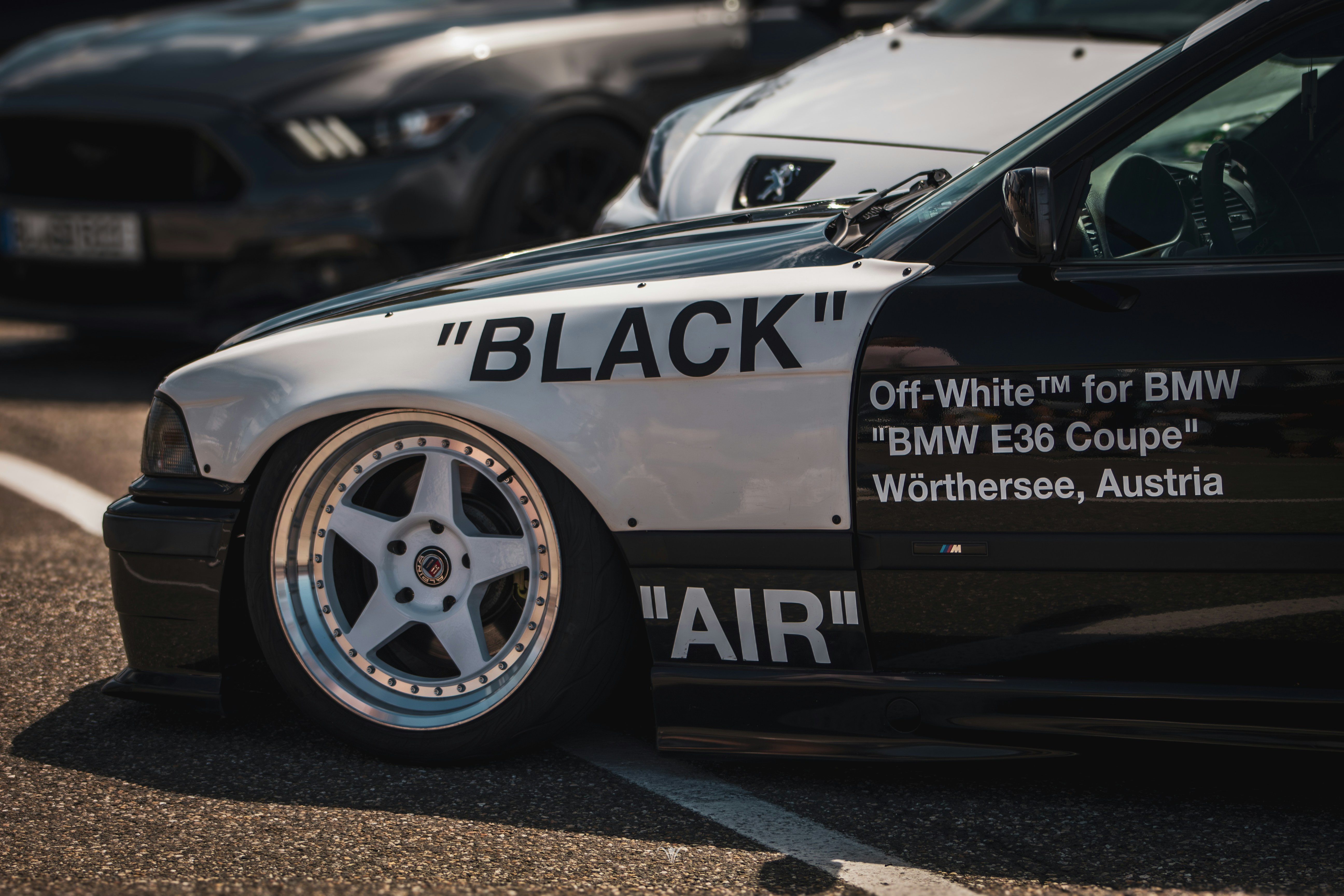 Wide-Wheel Statement: White BMW E36 Coupe with Bold Black Livery at a Car Meet