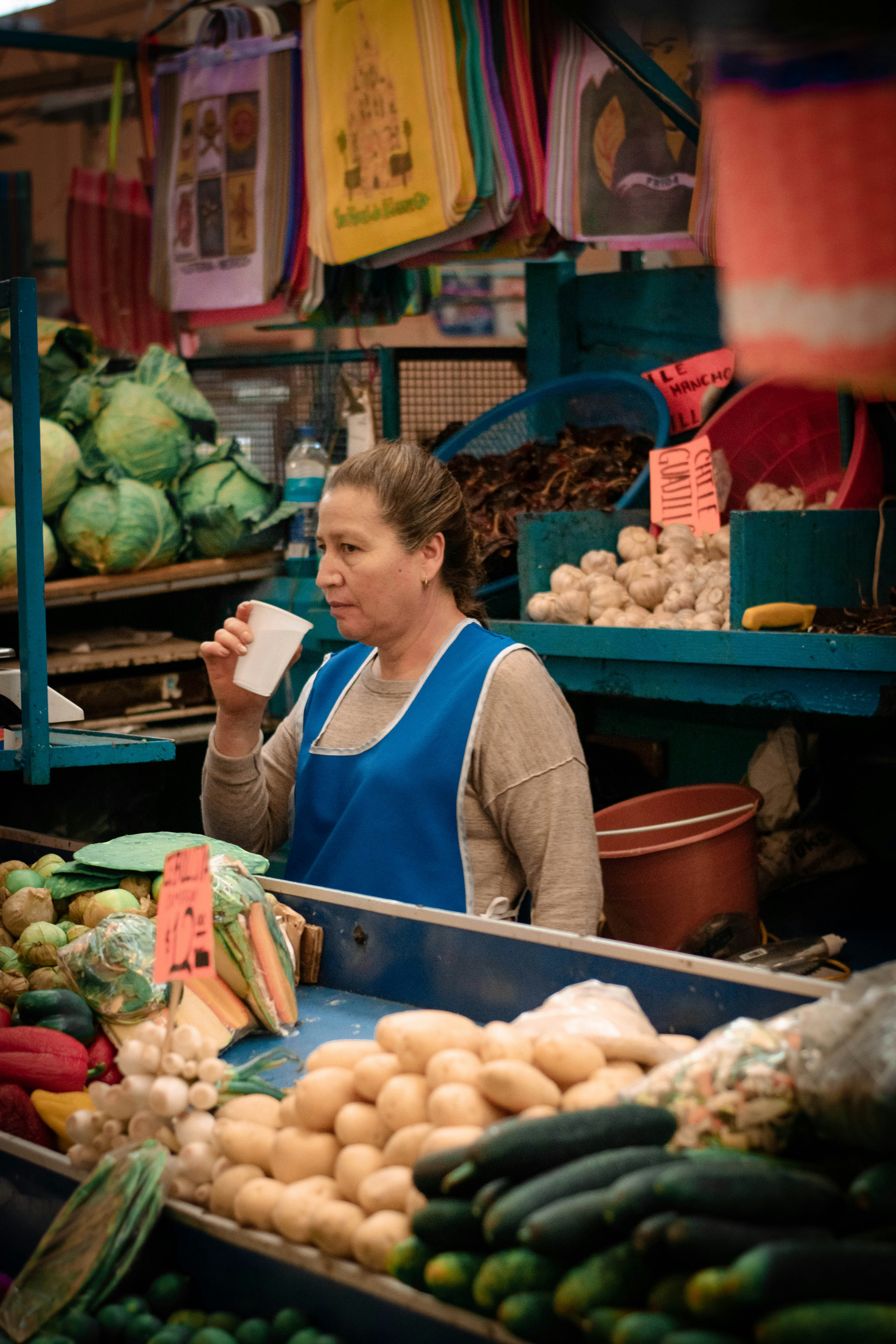 Cup in Hand at the Market: A Quiet Interlude Amid Stacks of Produce
