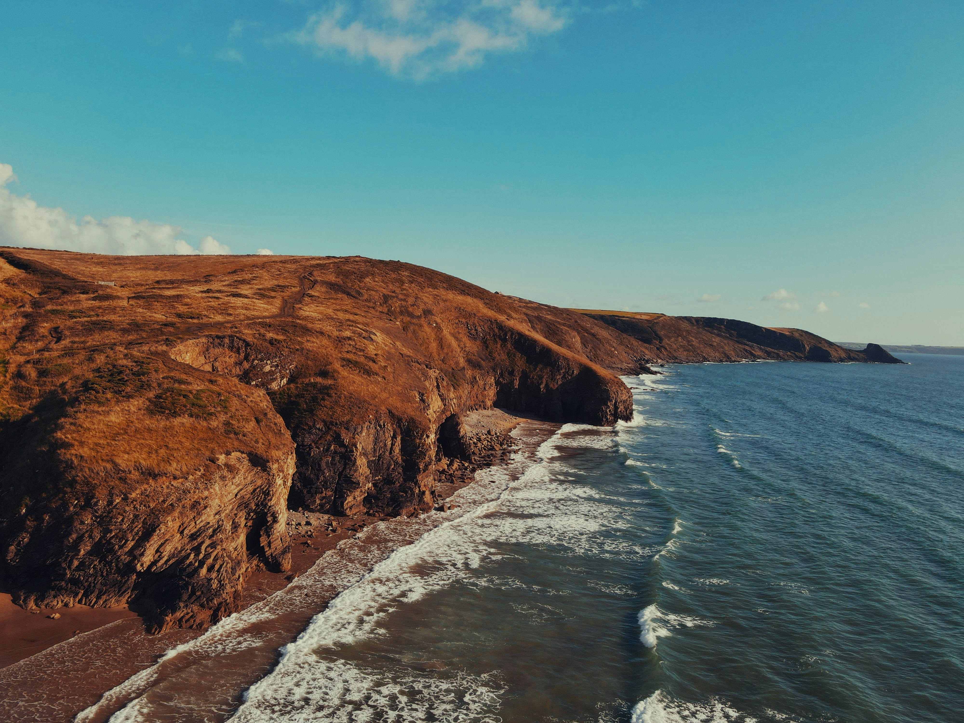 Coastal cliffs meet the ocean waves under a blue sky.