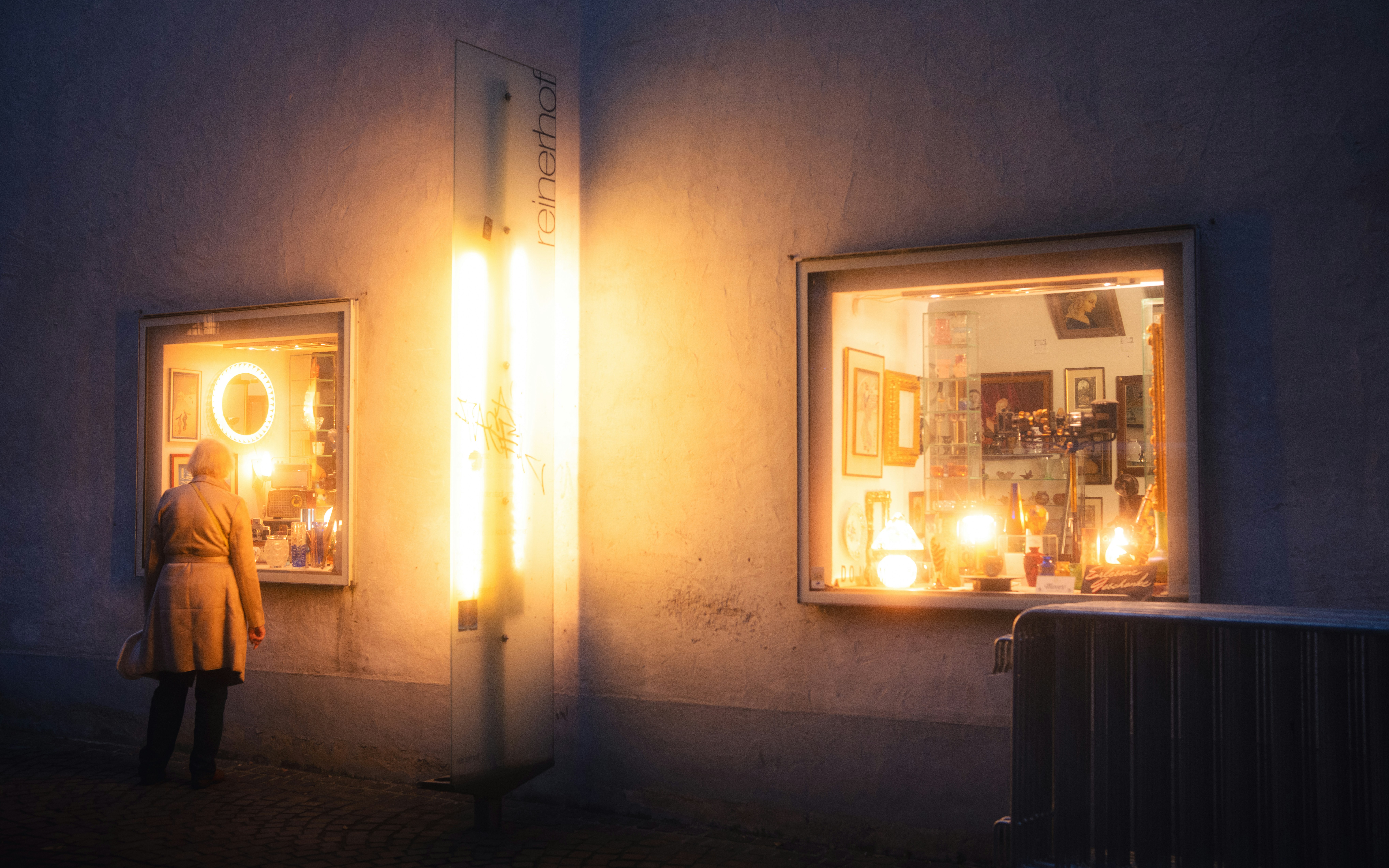 Woman looking into a brightly lit shop window at night.
