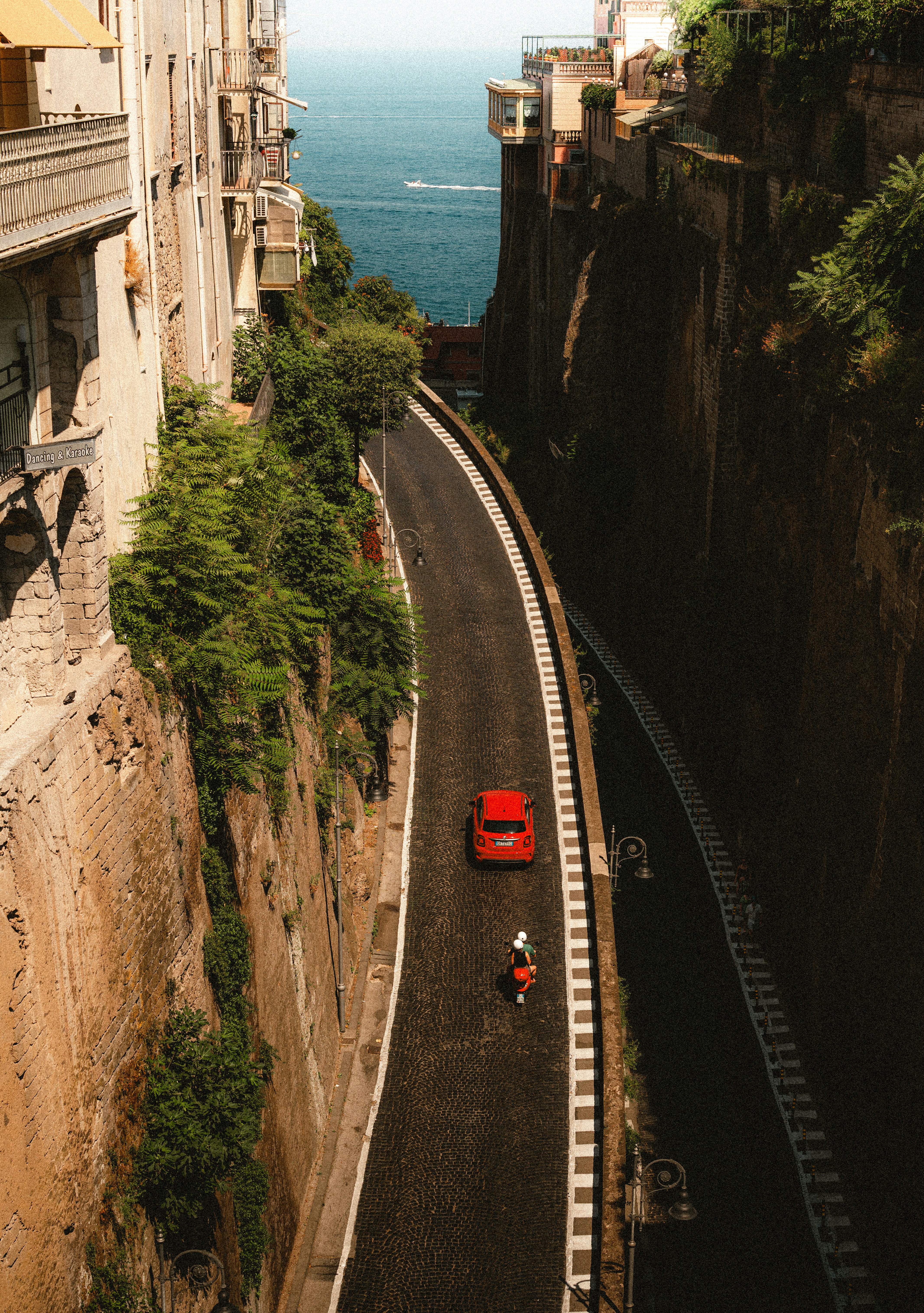 Red car and scooter on a coastal road.