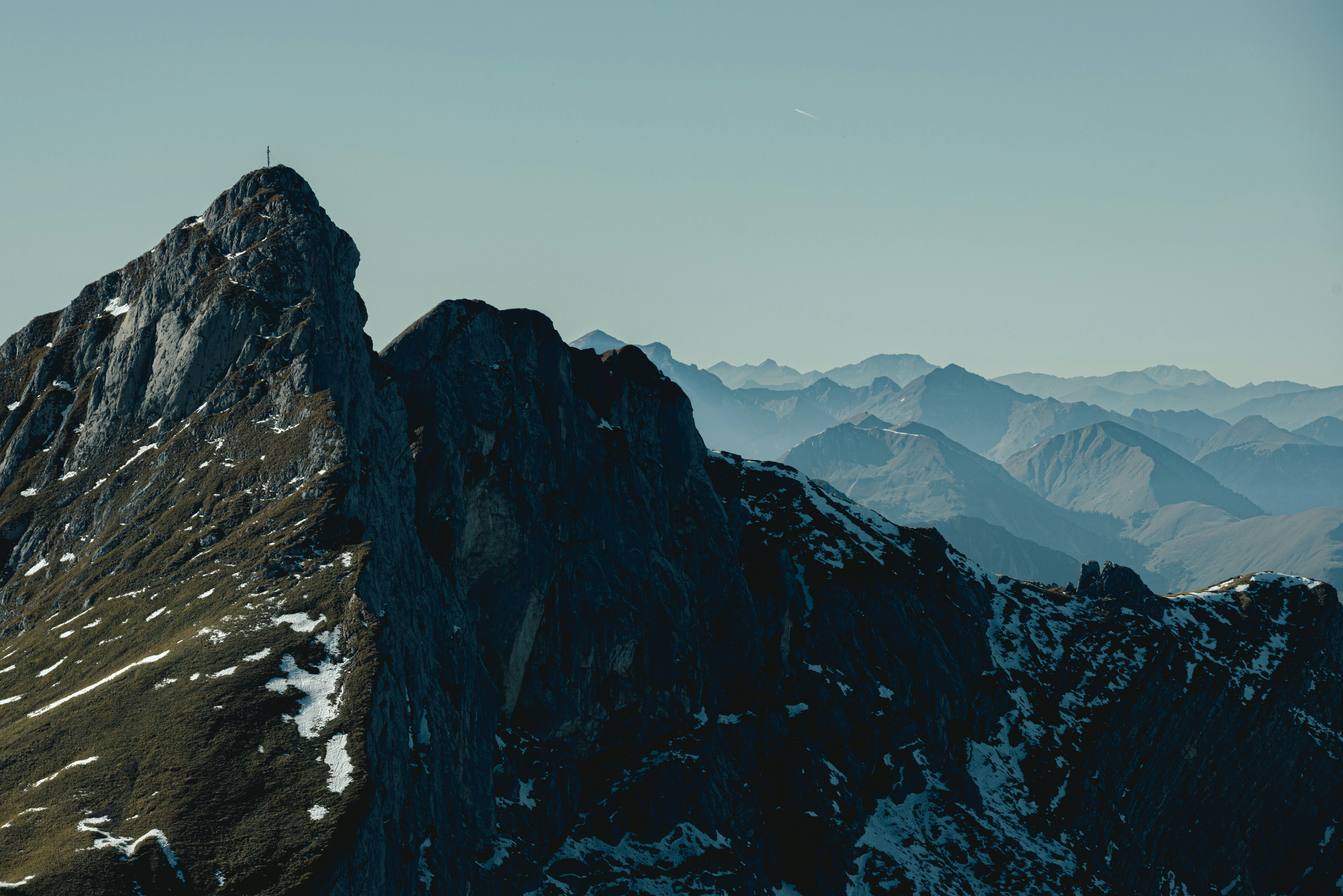 Sharp alpine peak in the Karwendel mountains during autumn. The dark rock ridge cuts dramatically through the pale valleys, under a crisp blue sky. Captured from a high vantage point with clear mountain light and strong contrast. | Jagged mountain peaks under a clear sky
