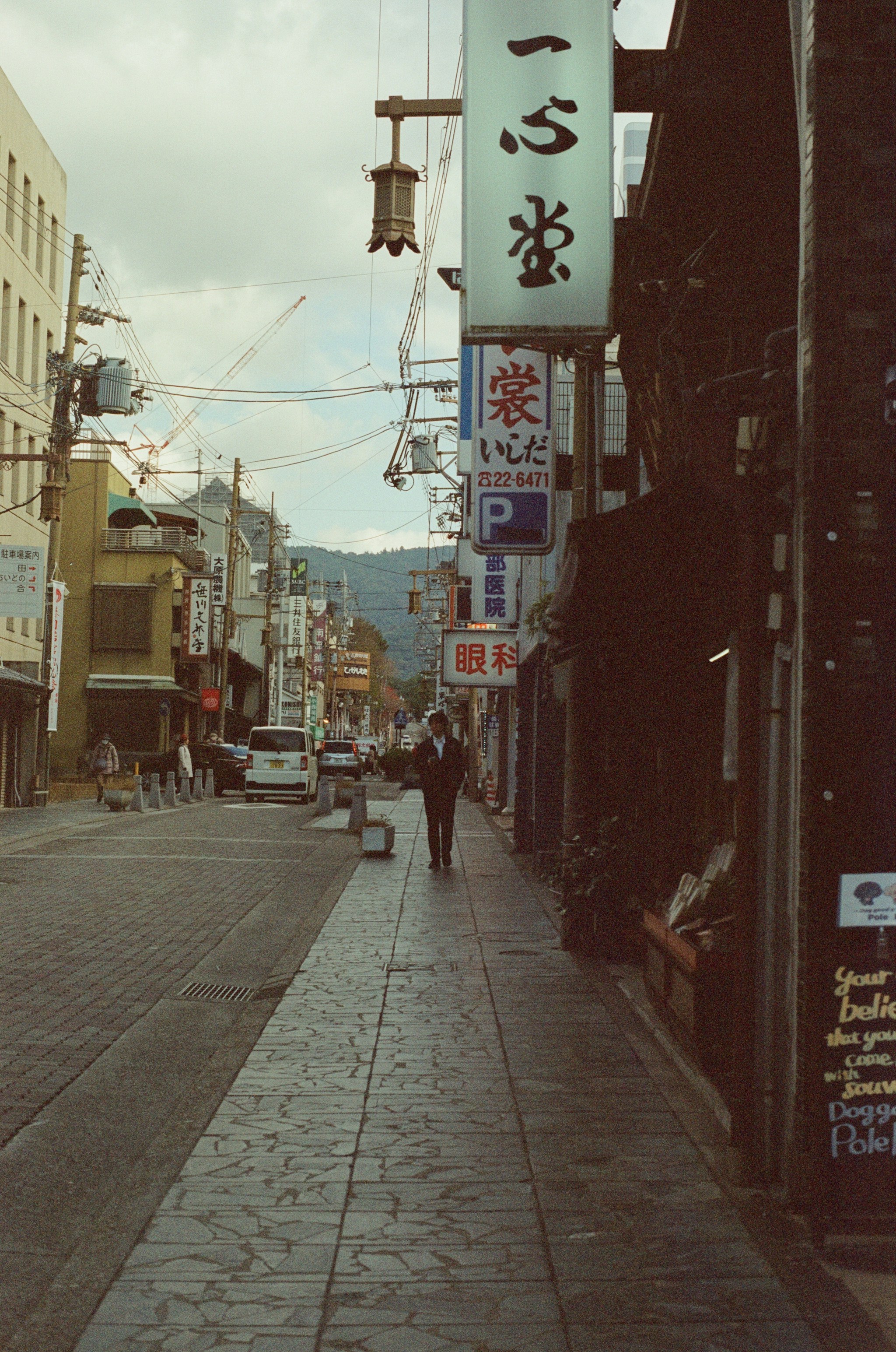 On 35mm film Kumo 250D | Man walks down a street with shops and signs.