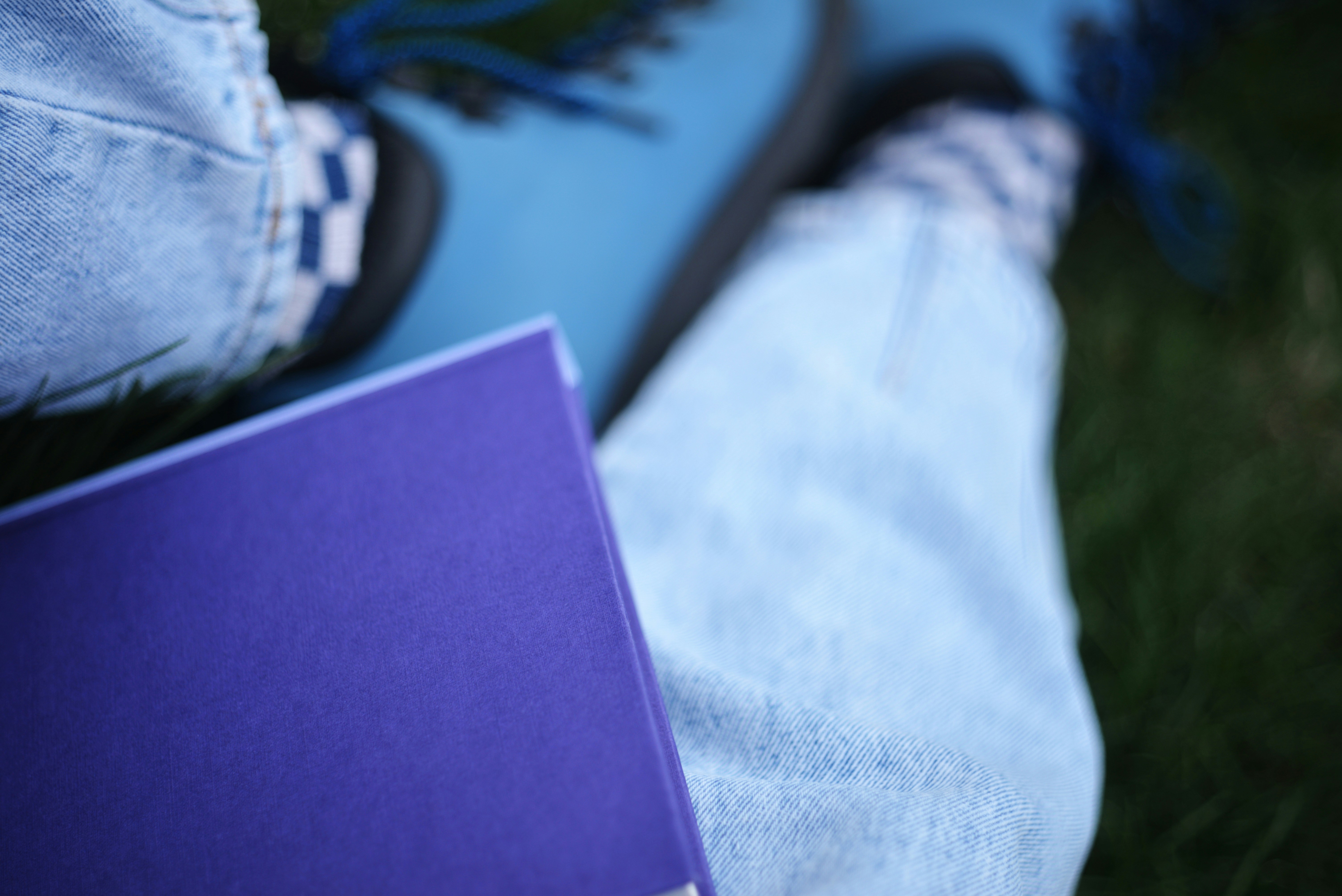 Person in jeans holding a purple book on grass