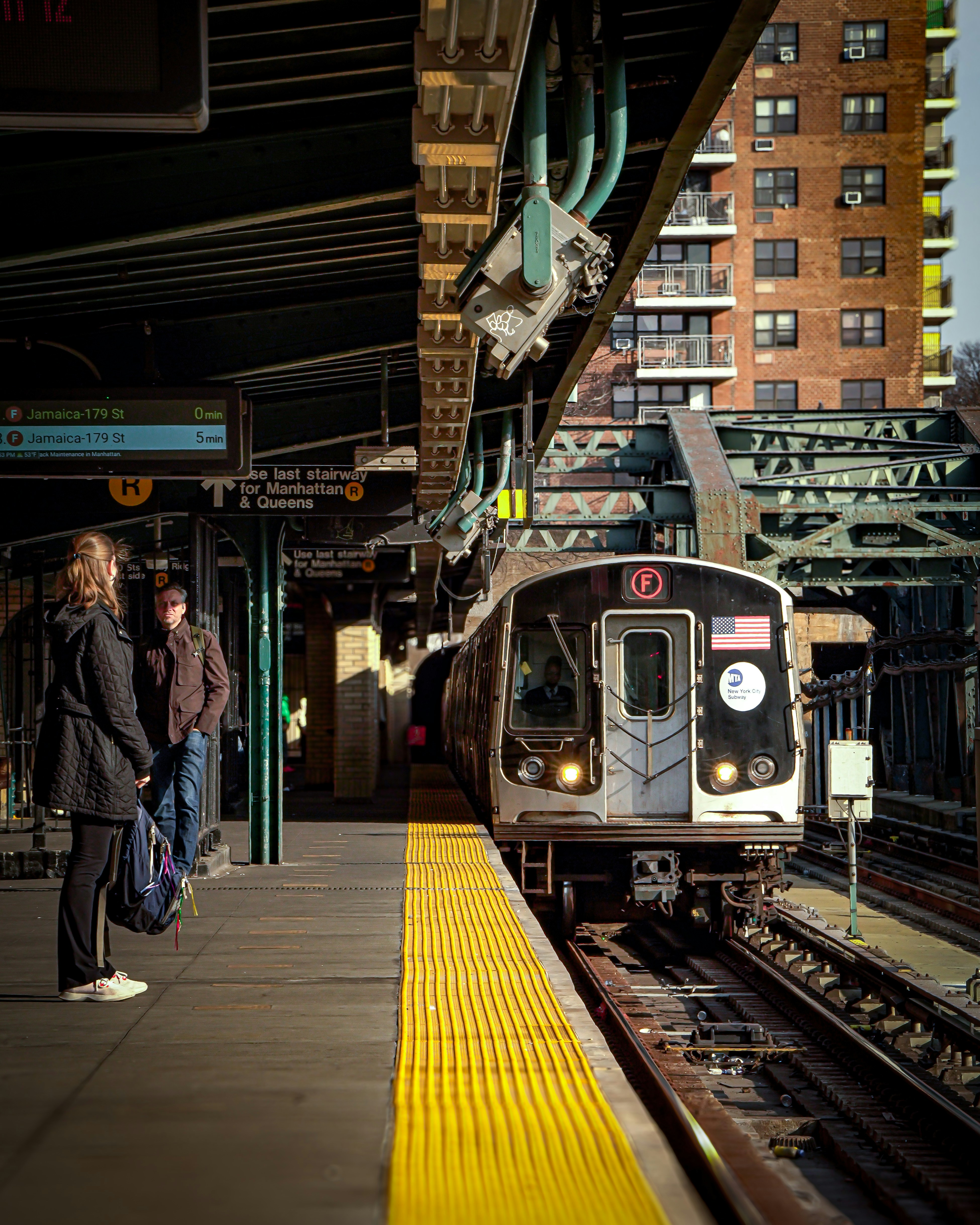 Front Car of a City Subway Approaches as Passengers Wait on a Sunlit Platform