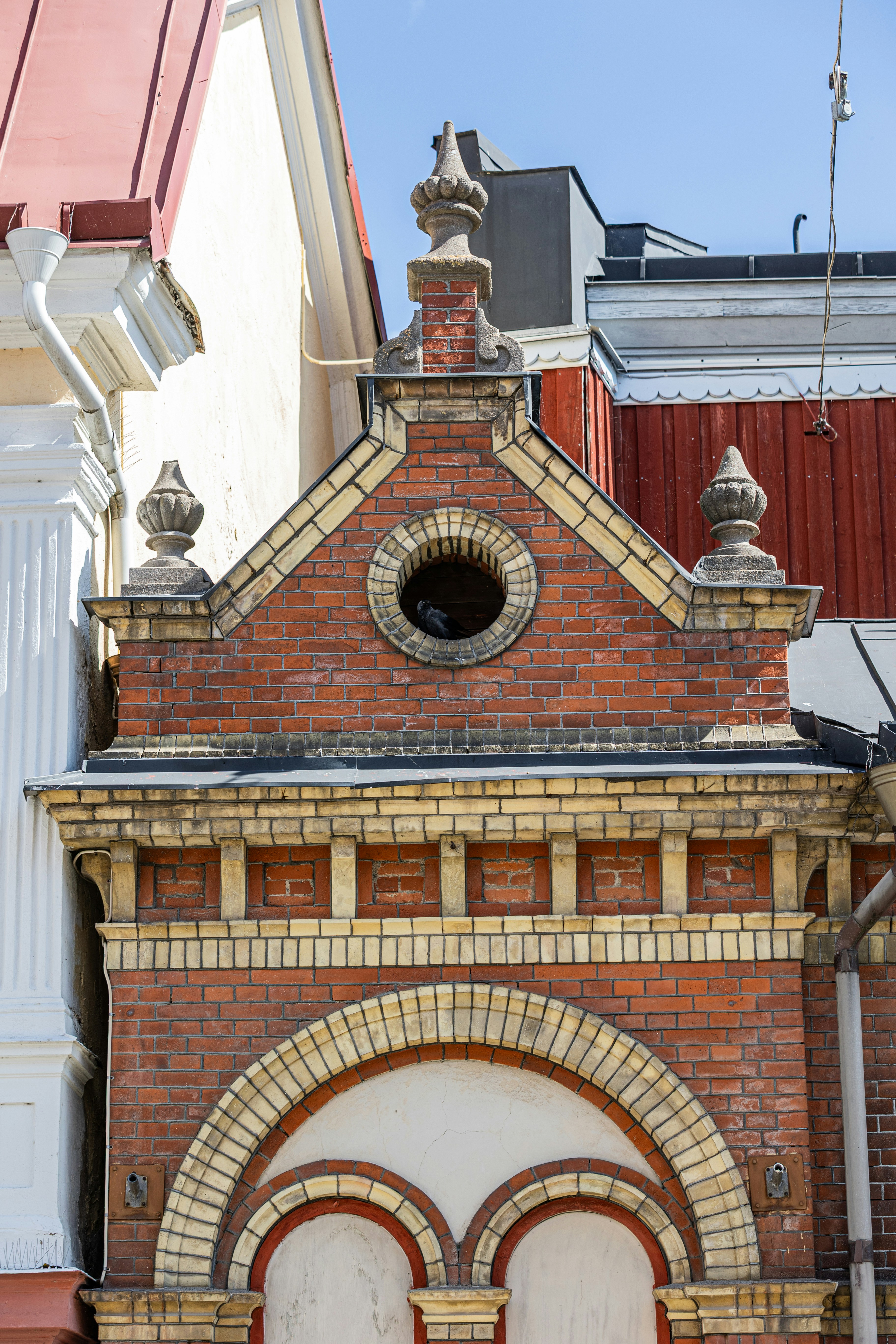 A jackdaw hides in a hole in the face of an ord building. | Ornate brick facade with arched windows and decorative details