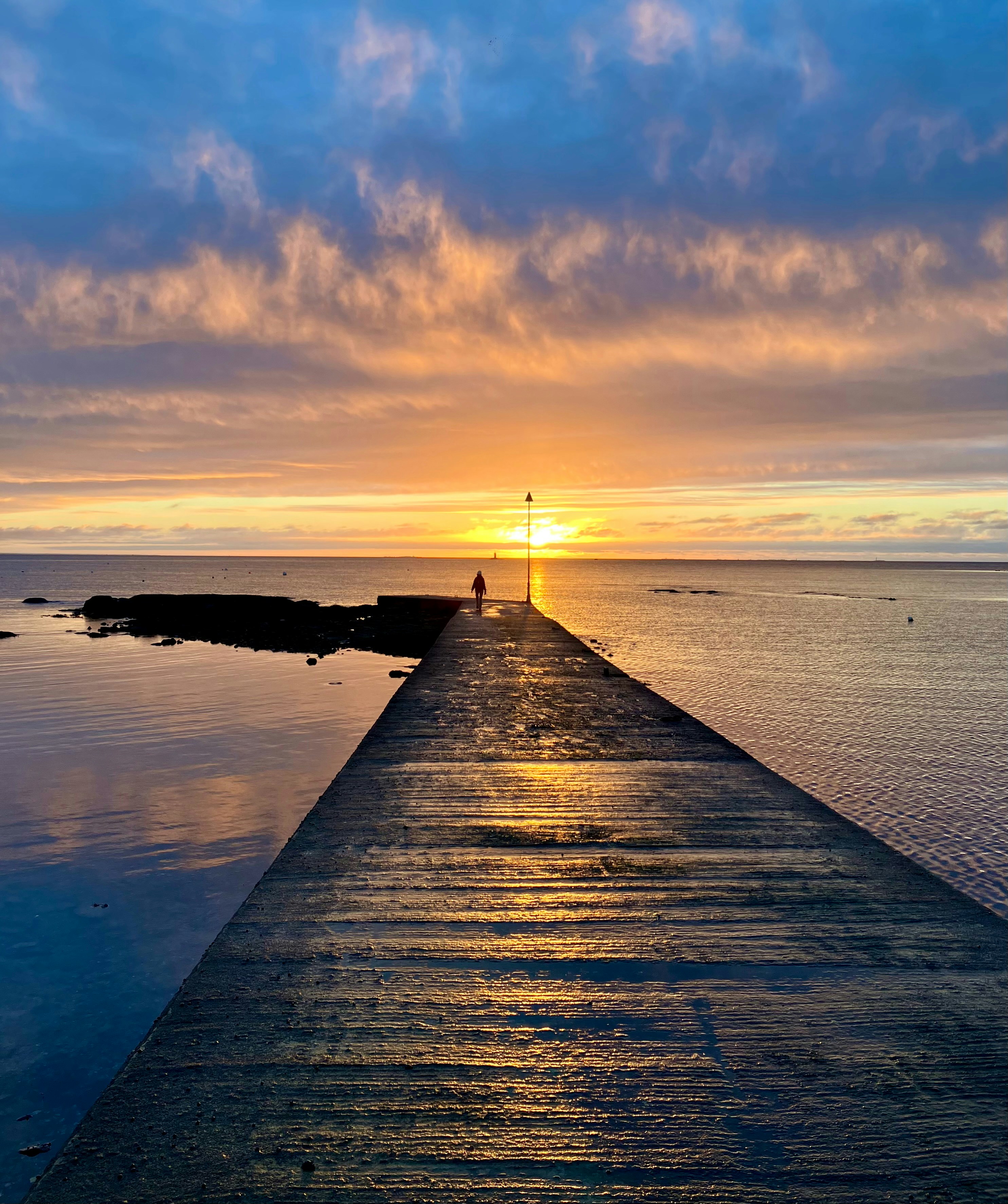 Person walking on a pier at sunset