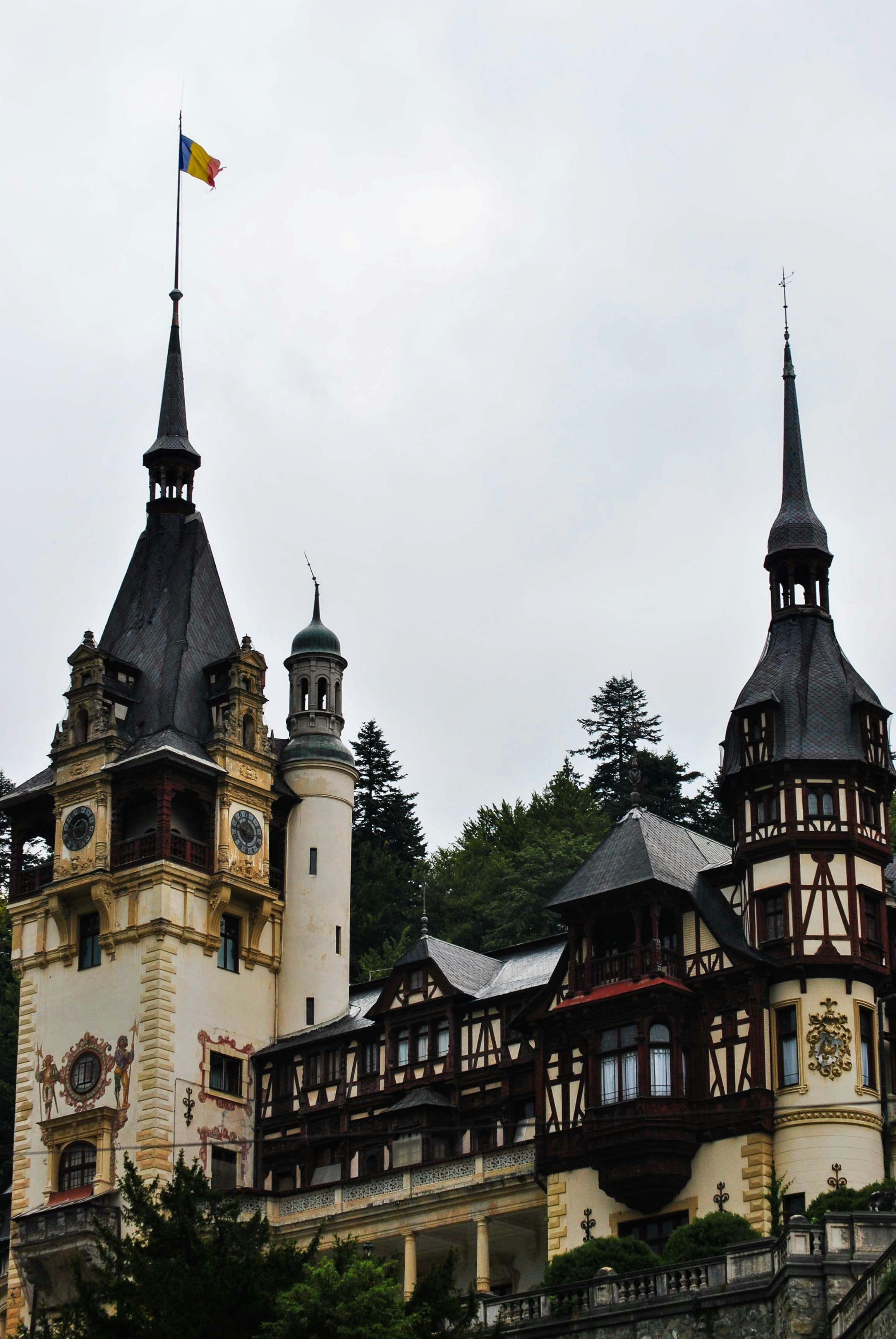 The Peleș Castle stands in all its architectural splendor, a masterpiece of Neo-Renaissance design nestled among the Carpathian Mountains.” | A grand castle with multiple towers and a flag.
