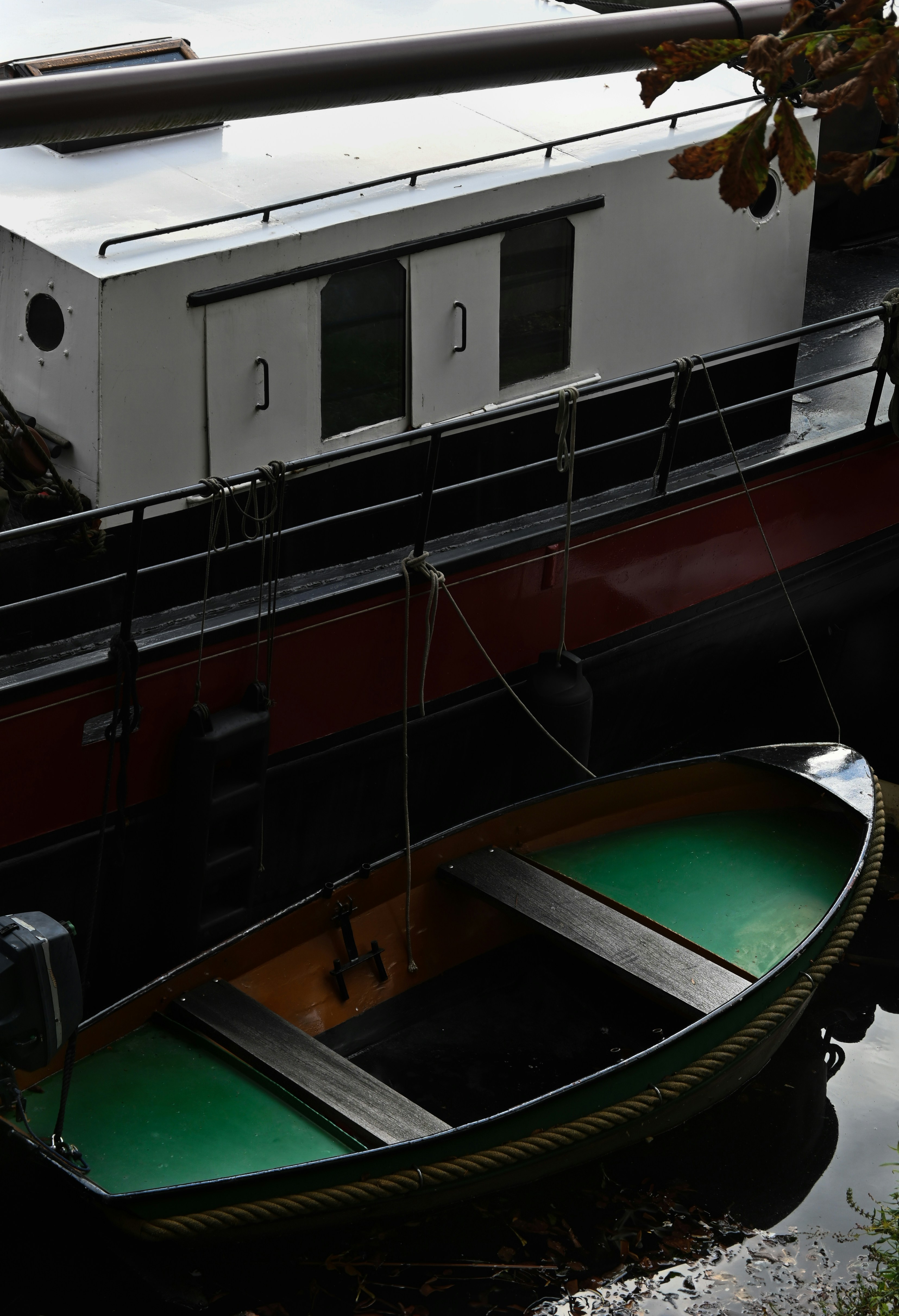 A small green rowboat tied to a larger moored boat.