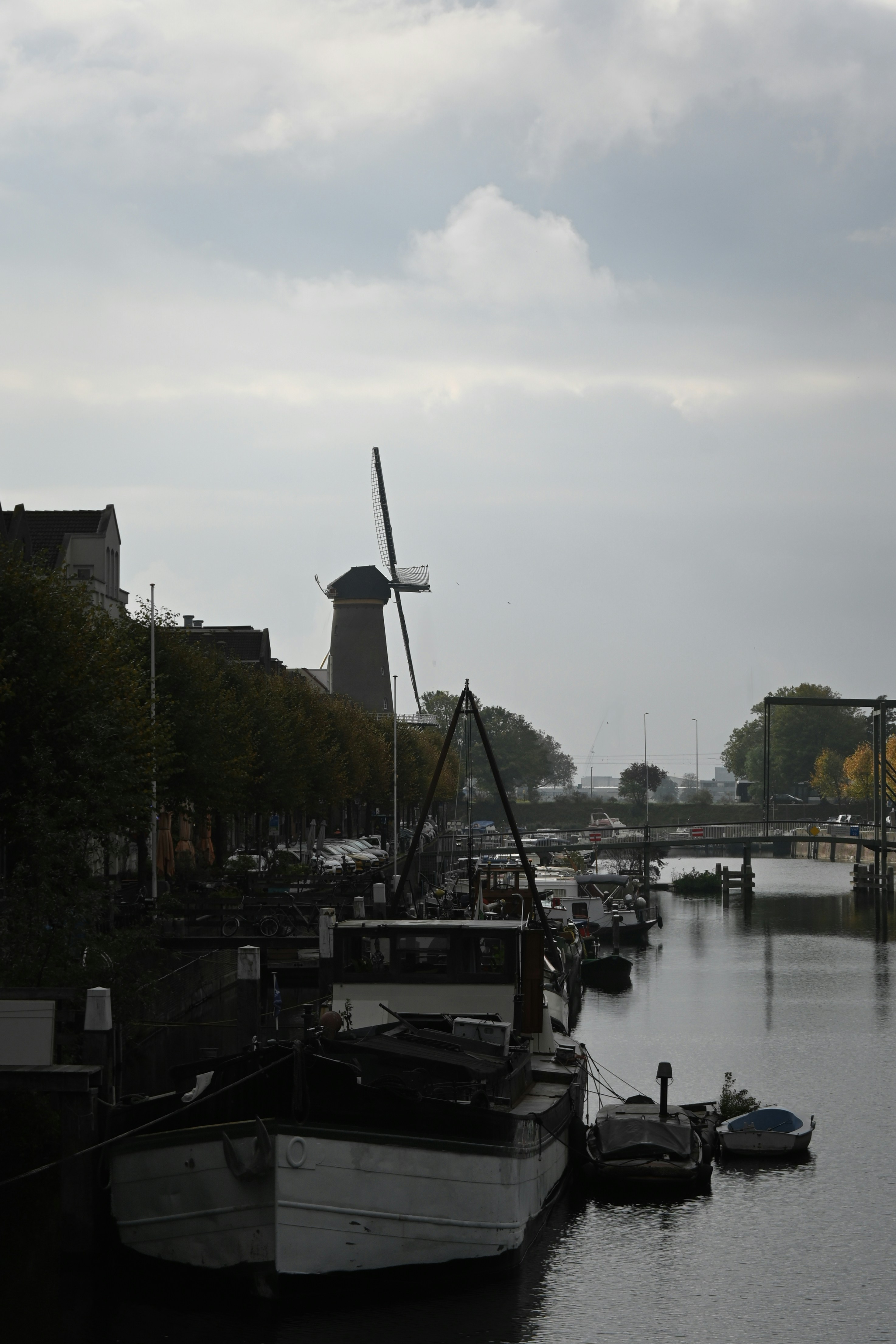 Boats docked on a canal with a windmill.