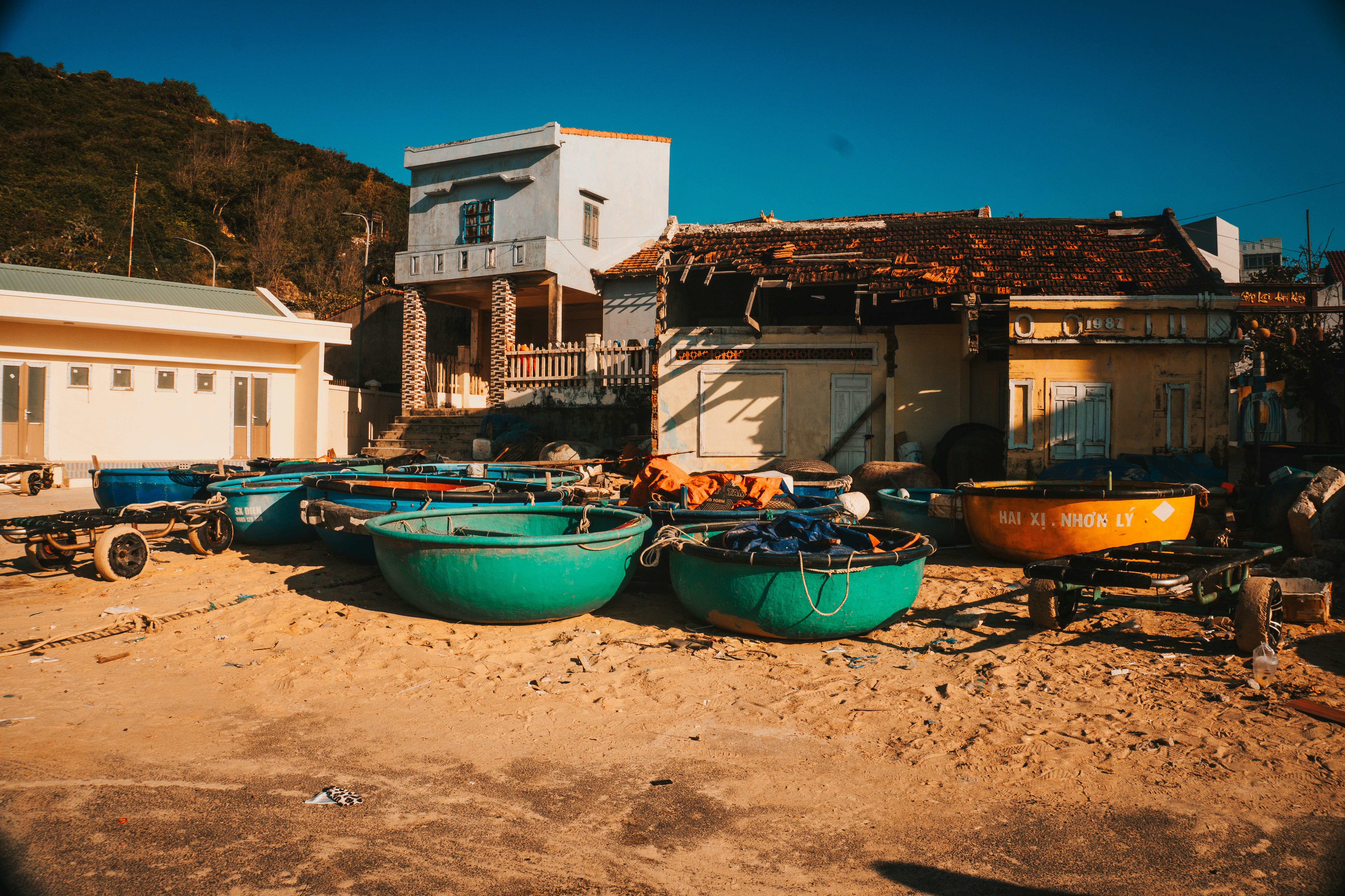 Round fishing boats rest on sandy shore near buildings.