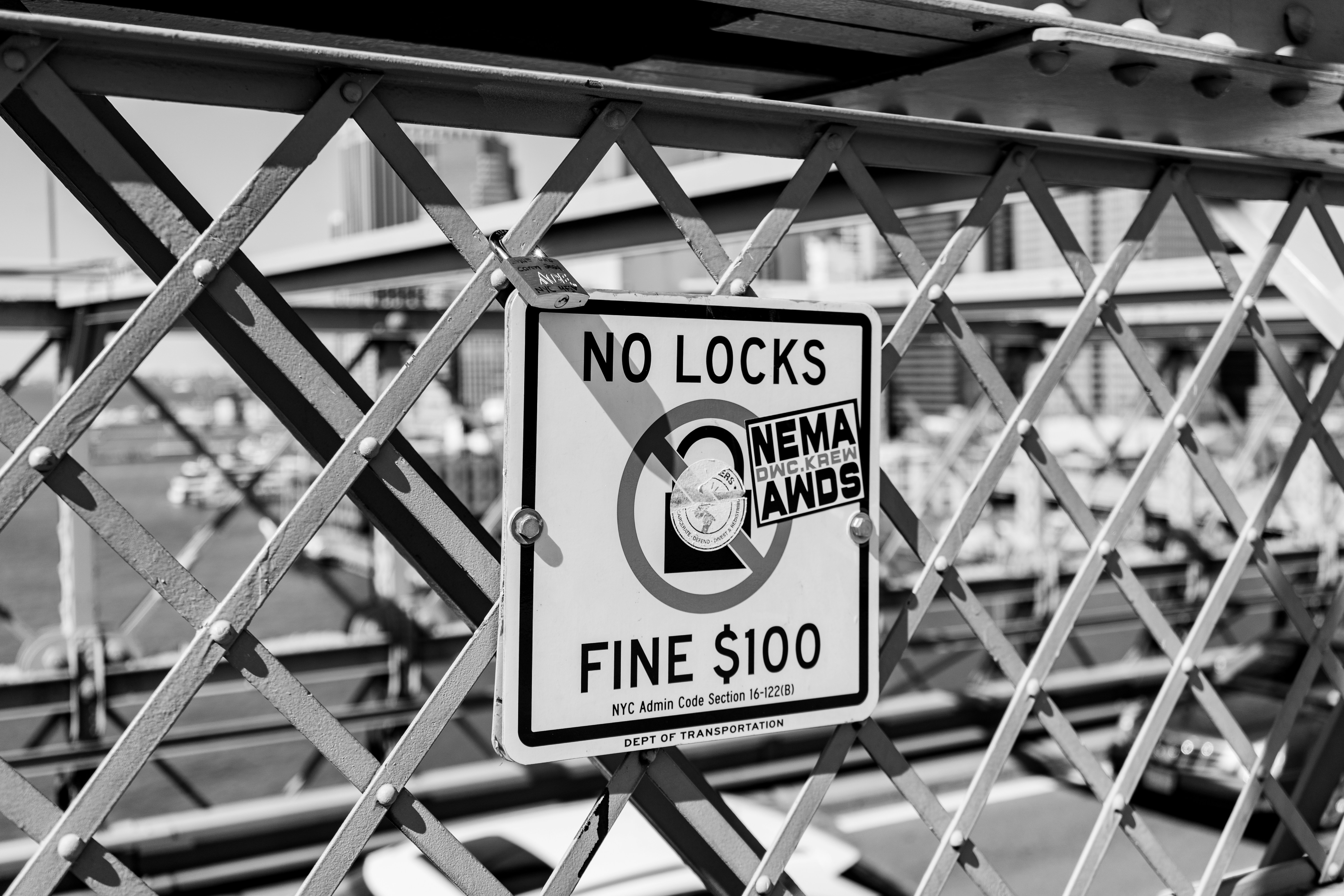 Sign prohibiting locks on a bridge, emphasizing urban regulations against love padlocks. Black and white tones enhance the industrial feel.
