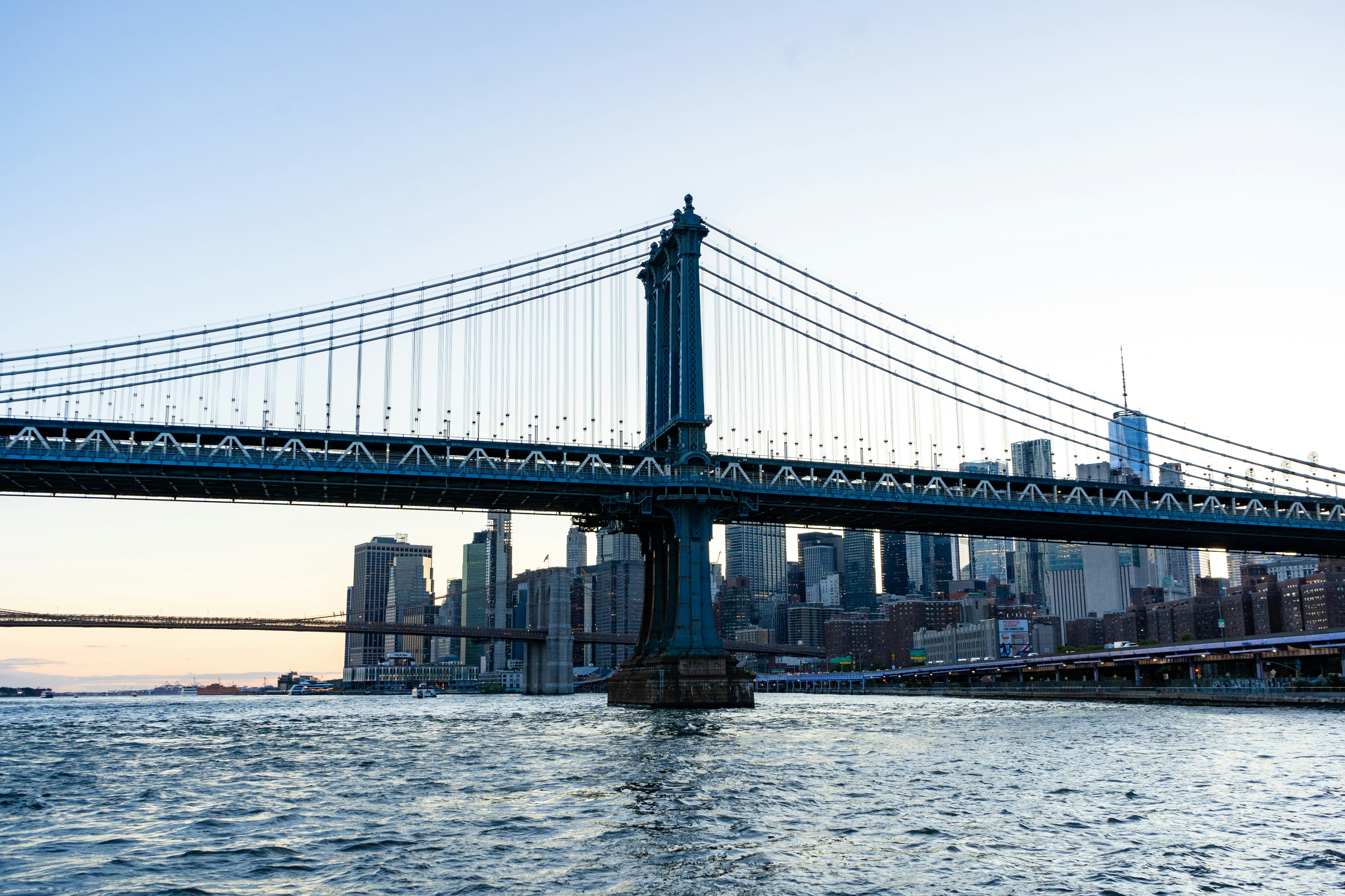 Manhattan Bridge arching gracefully over the East River, framed by the New York City skyline at dusk.