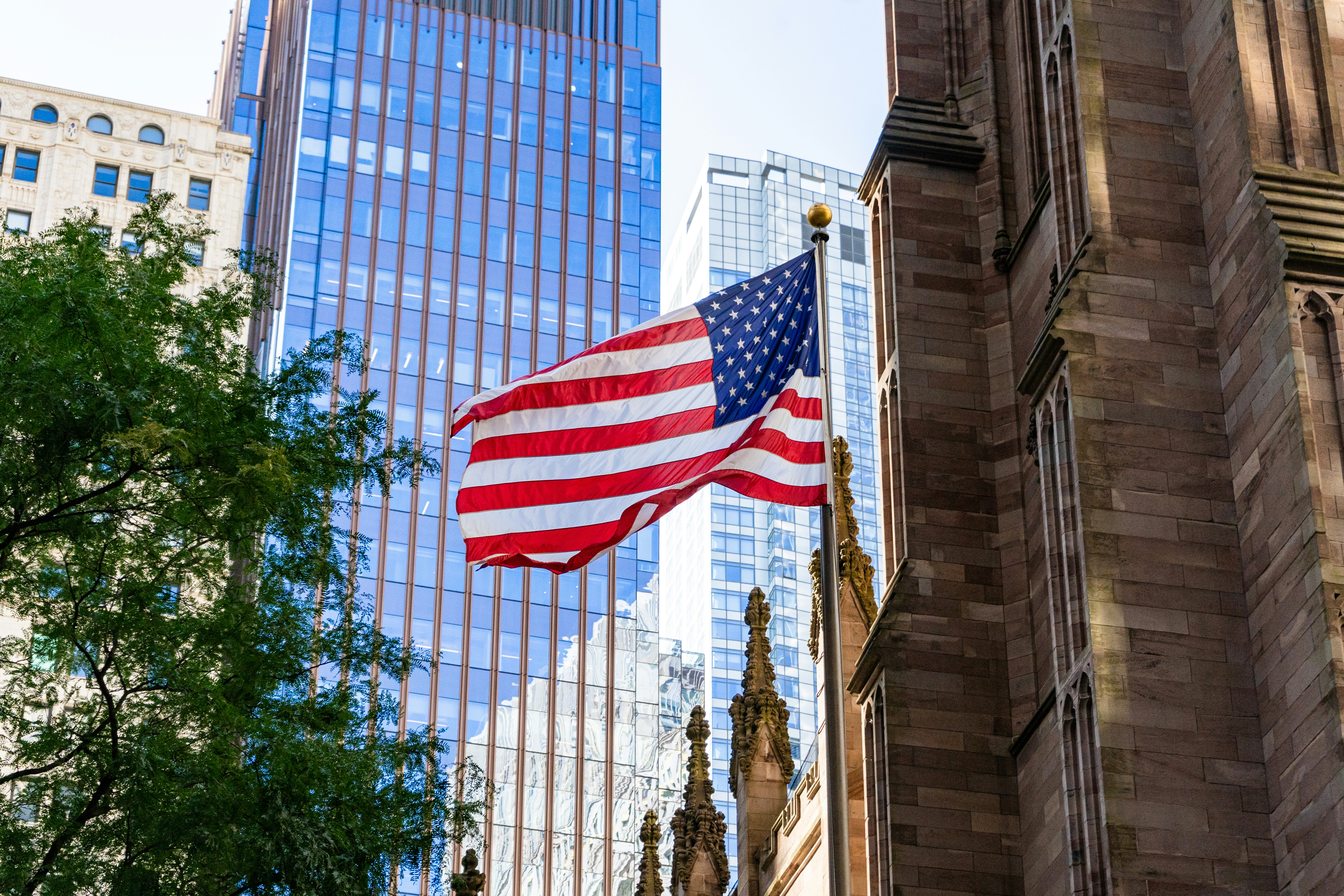 American flag waving amidst towering skyscrapers and historic architecture, showcasing a blend of tradition and contemporary design.
