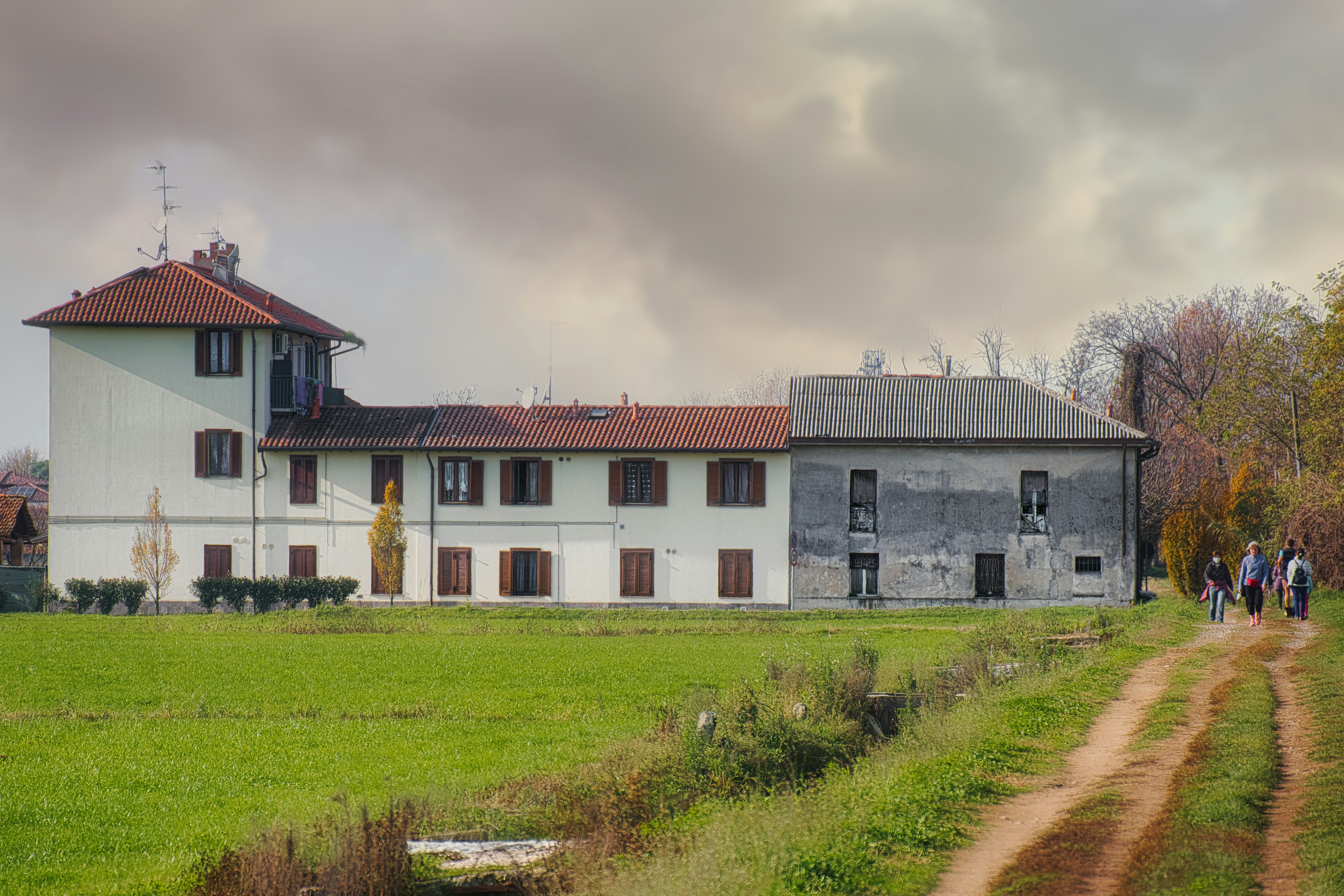 Old farmhouse | People walk on a dirt path beside a building.