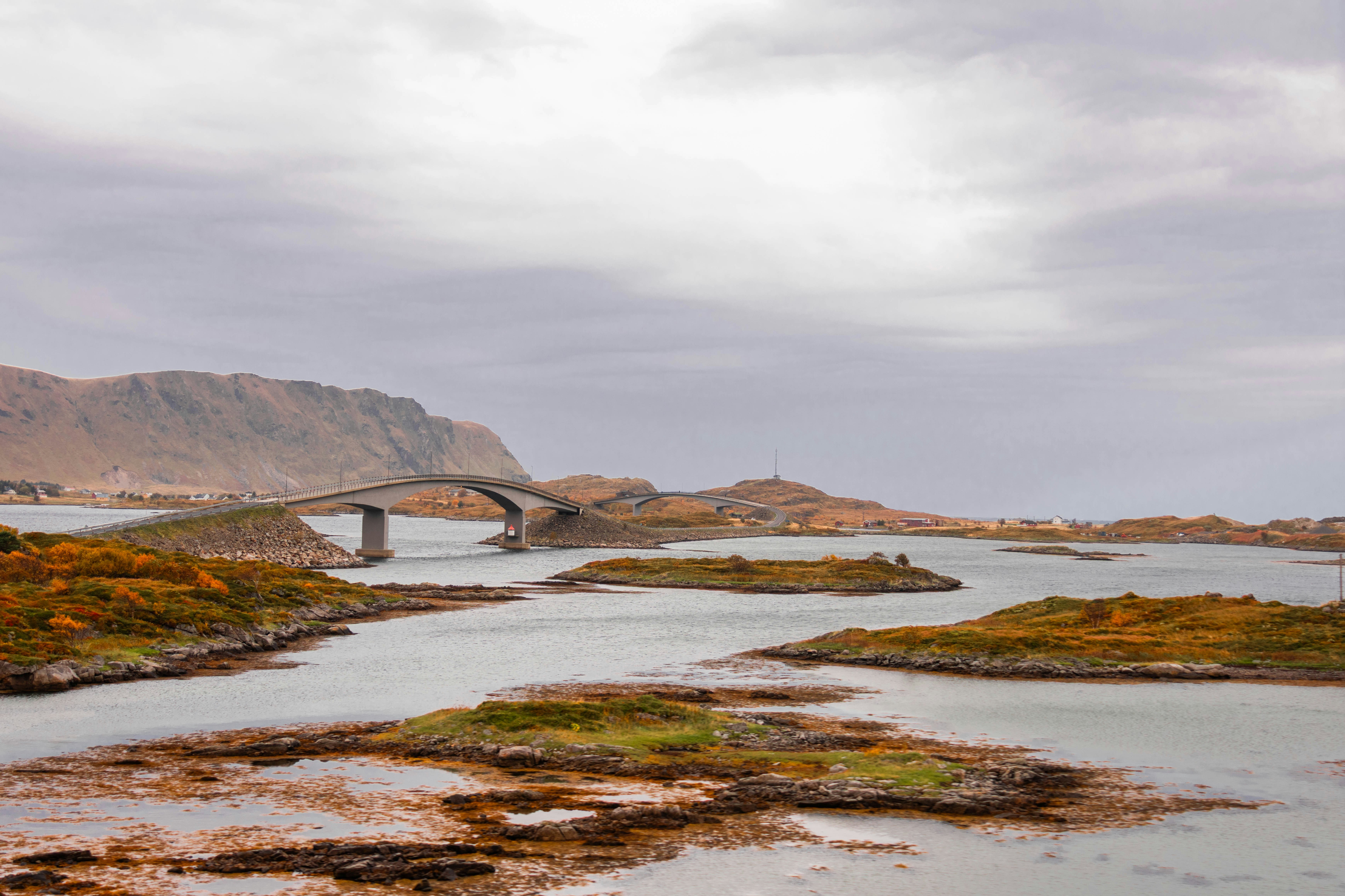 A modern bridge gracefully arches over a winding waterway, surrounded by rugged landscapes and autumnal hues. The scene conveys a sense of tranquility and connection.