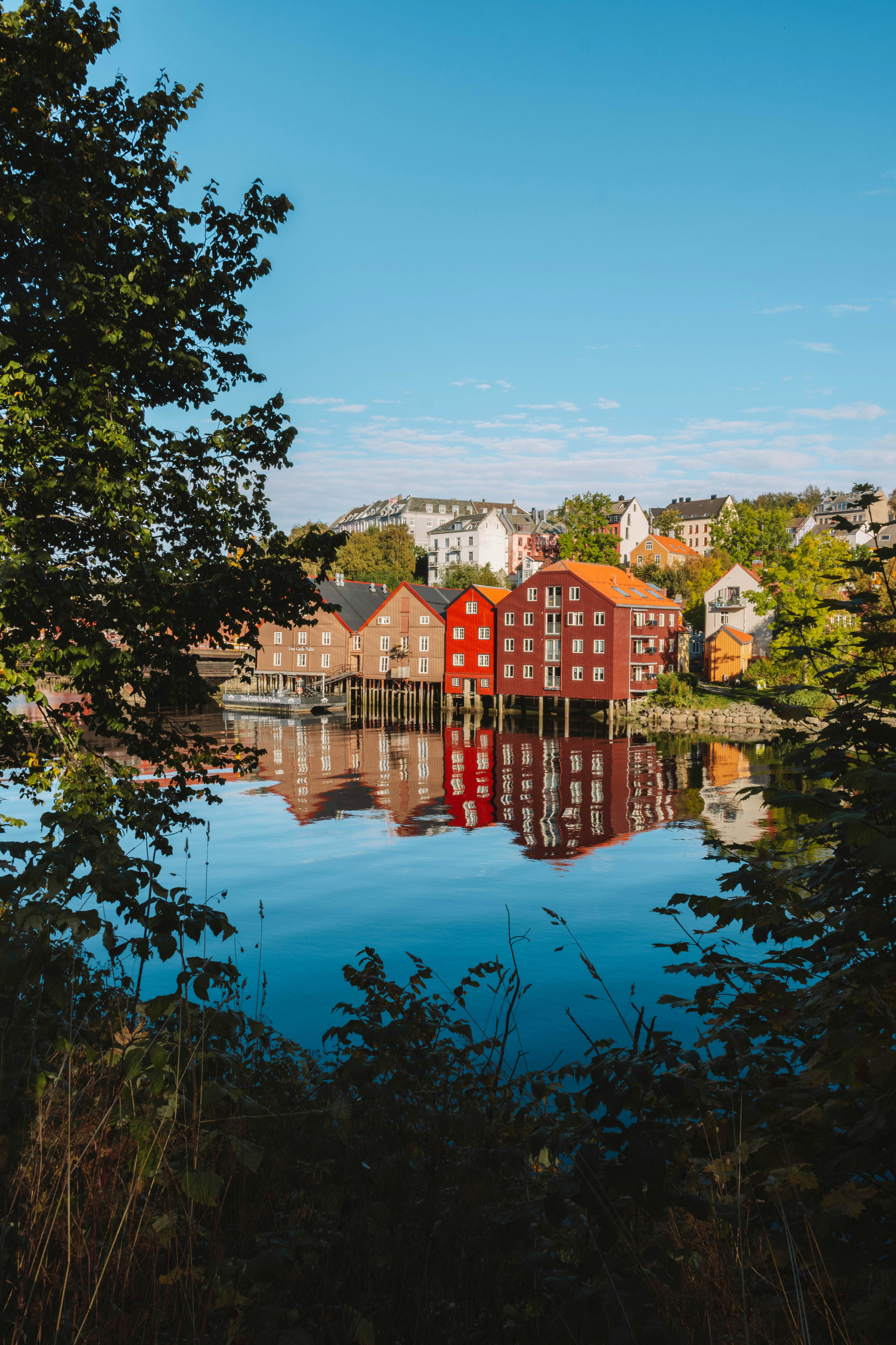 Historic wooden houses with vibrant colors reflected in a tranquil lake, framed by lush greenery.
