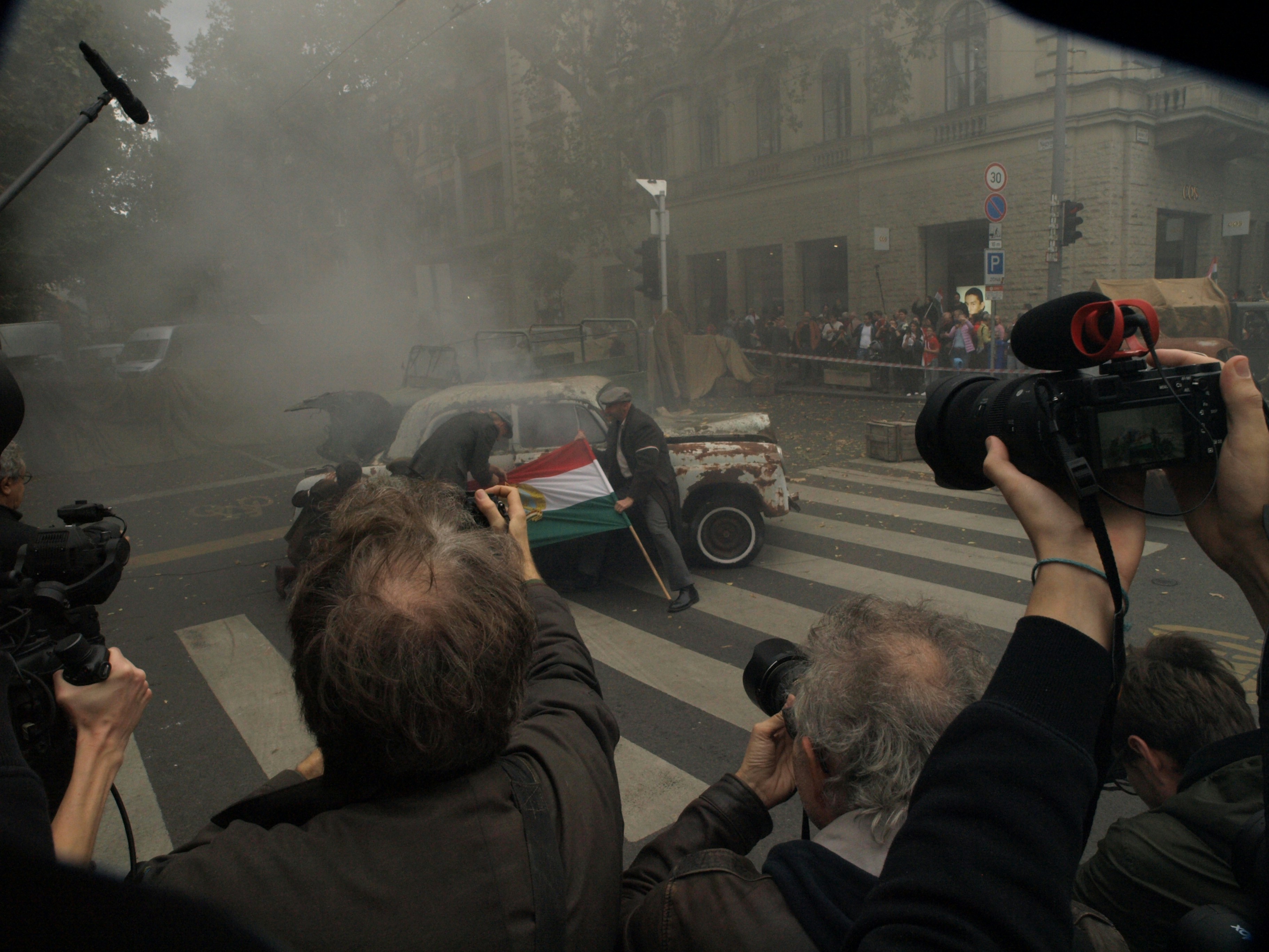 Crowd photographs burning car with hungarian flag.