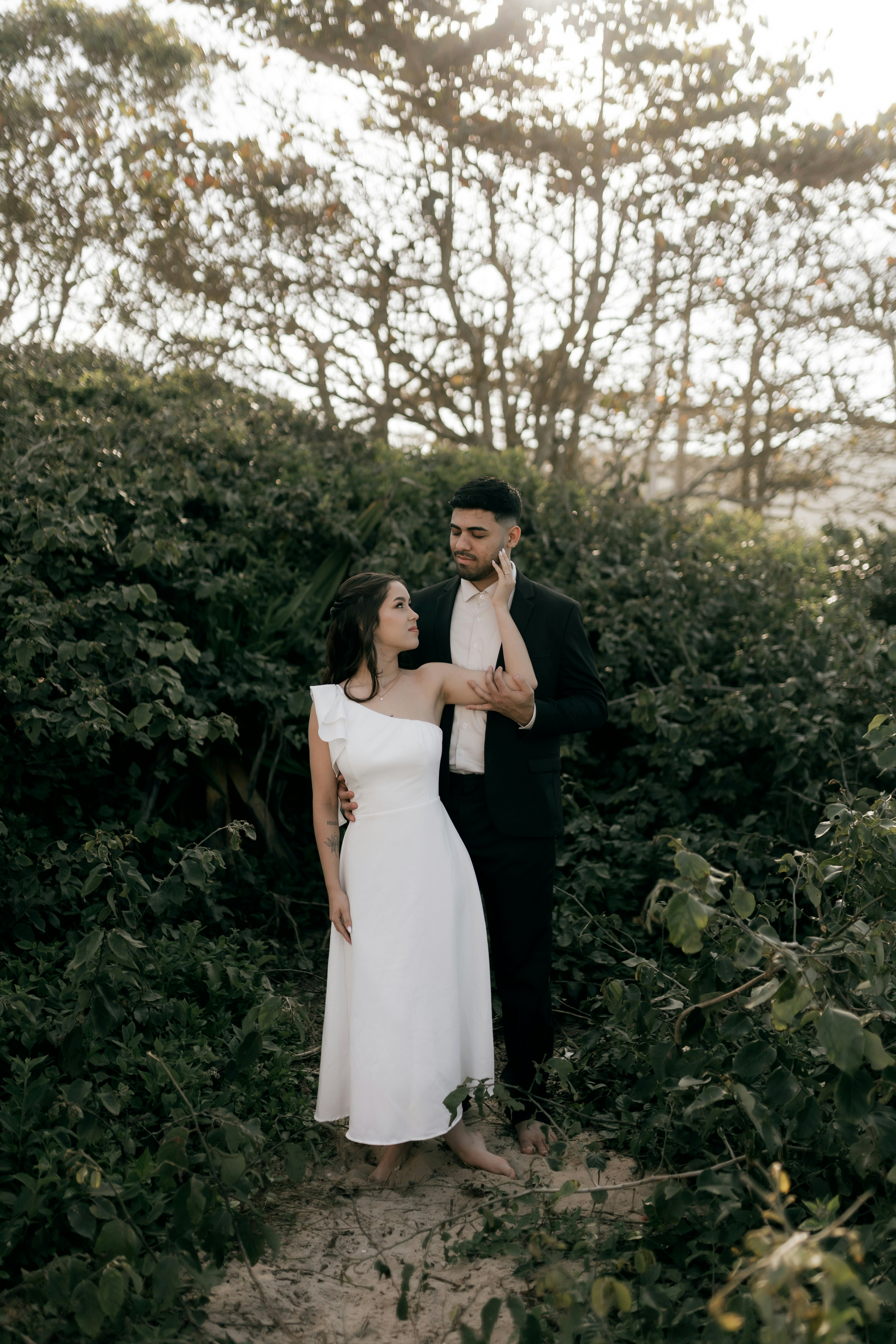 Couple in formal wear stands in lush green foliage