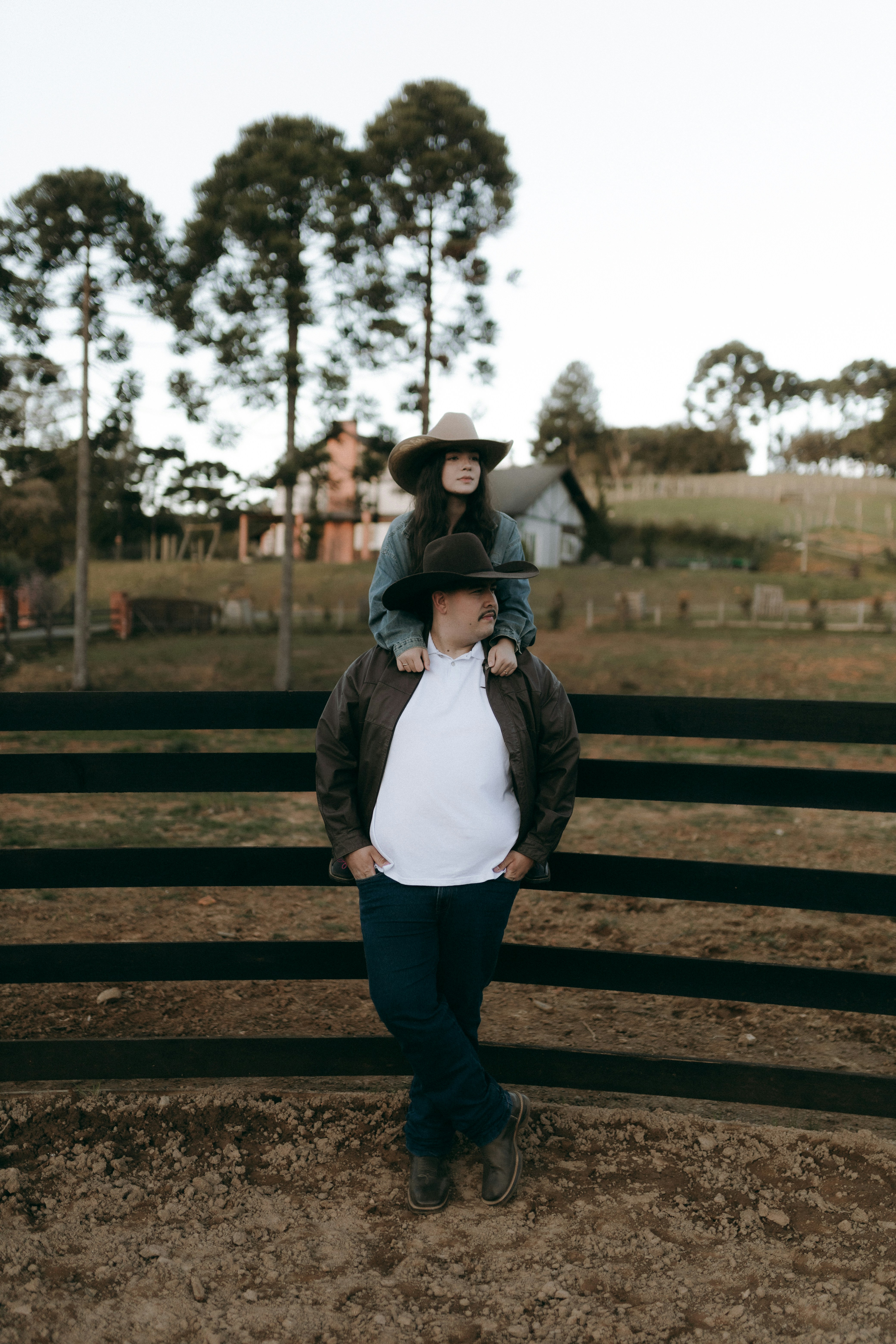 Couple wearing cowboy hats by wooden fence