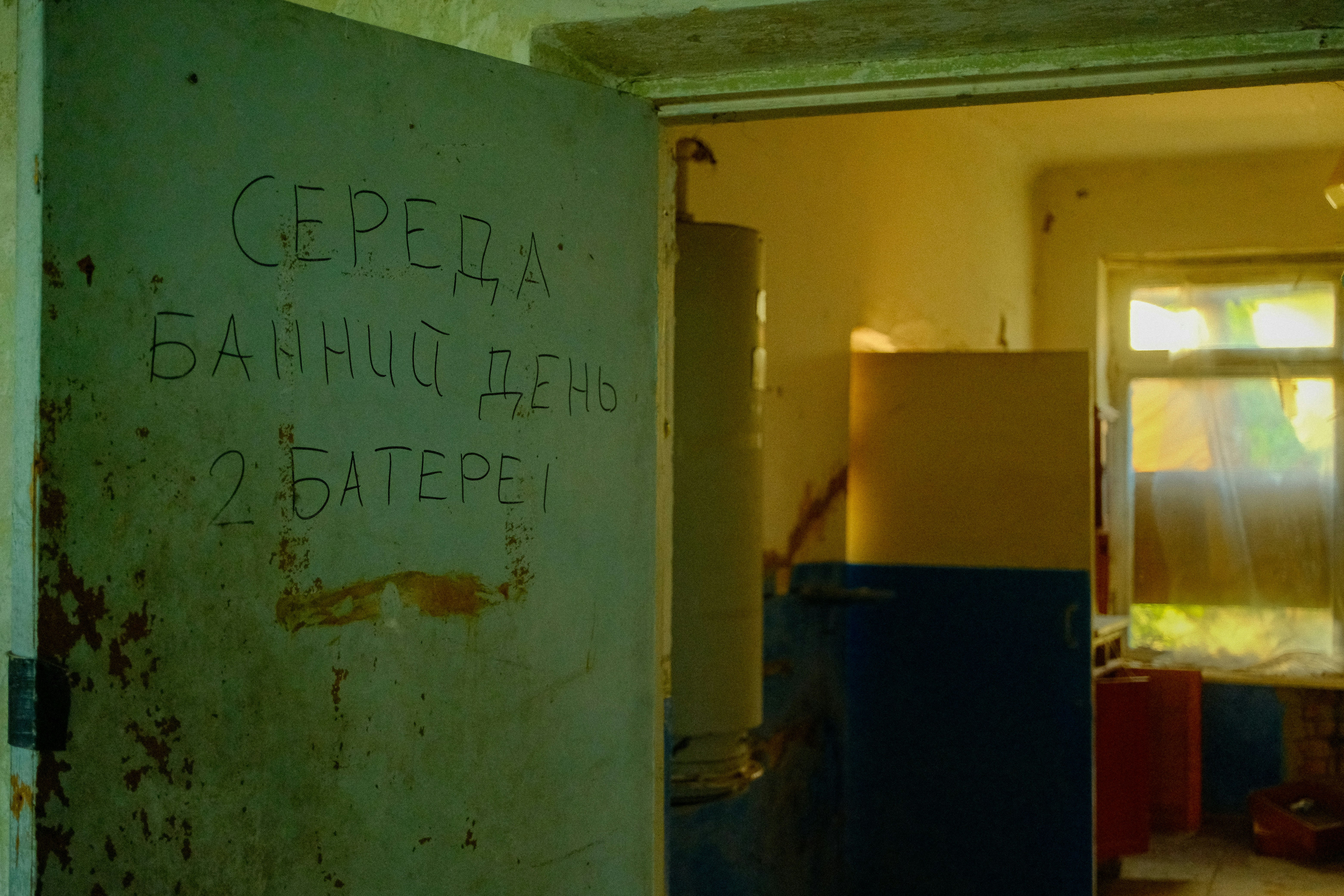 Rusty door with handwritten notes in a dimly lit, abandoned room showcasing peeling paint and remnants of past use.