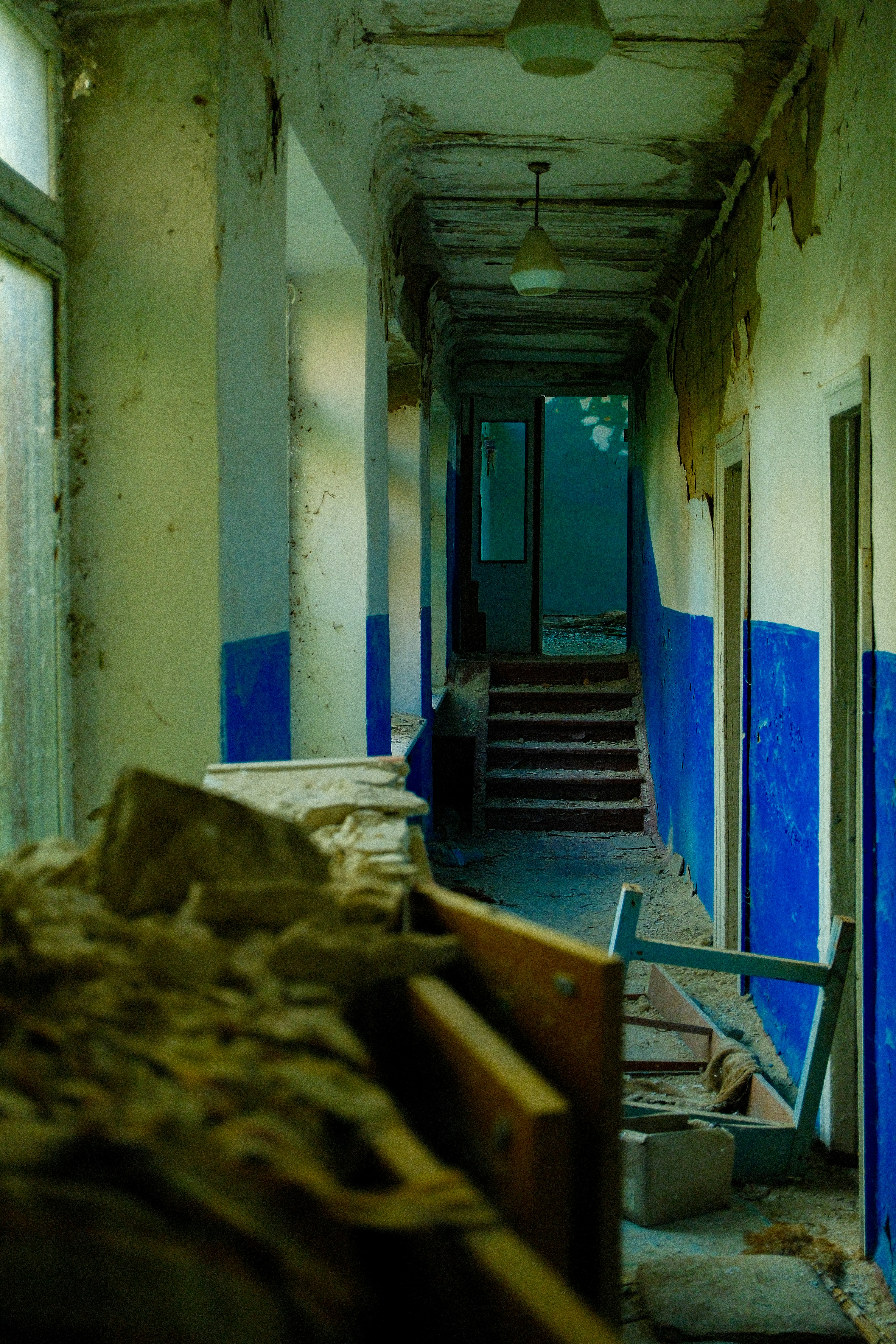 Desolate hallway with peeling paint and scattered debris, leading to a shadowy entrance. The remnants of a once vibrant space tell a story of neglect.