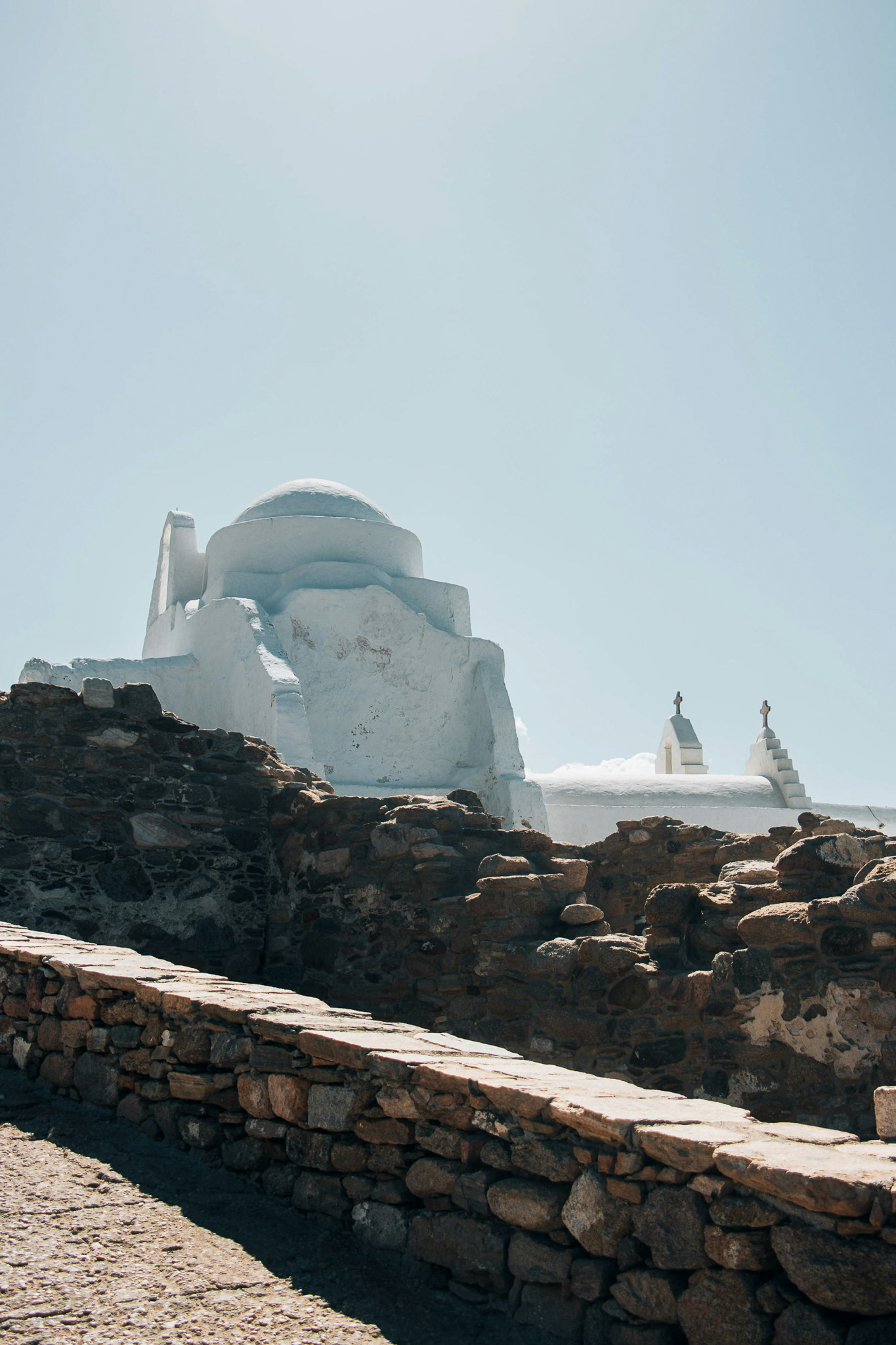 The whitewashed beauty of Panagia Paraportiani in Mykonos, glowing under the Aegean sun. | White domed church ruins against a clear sky