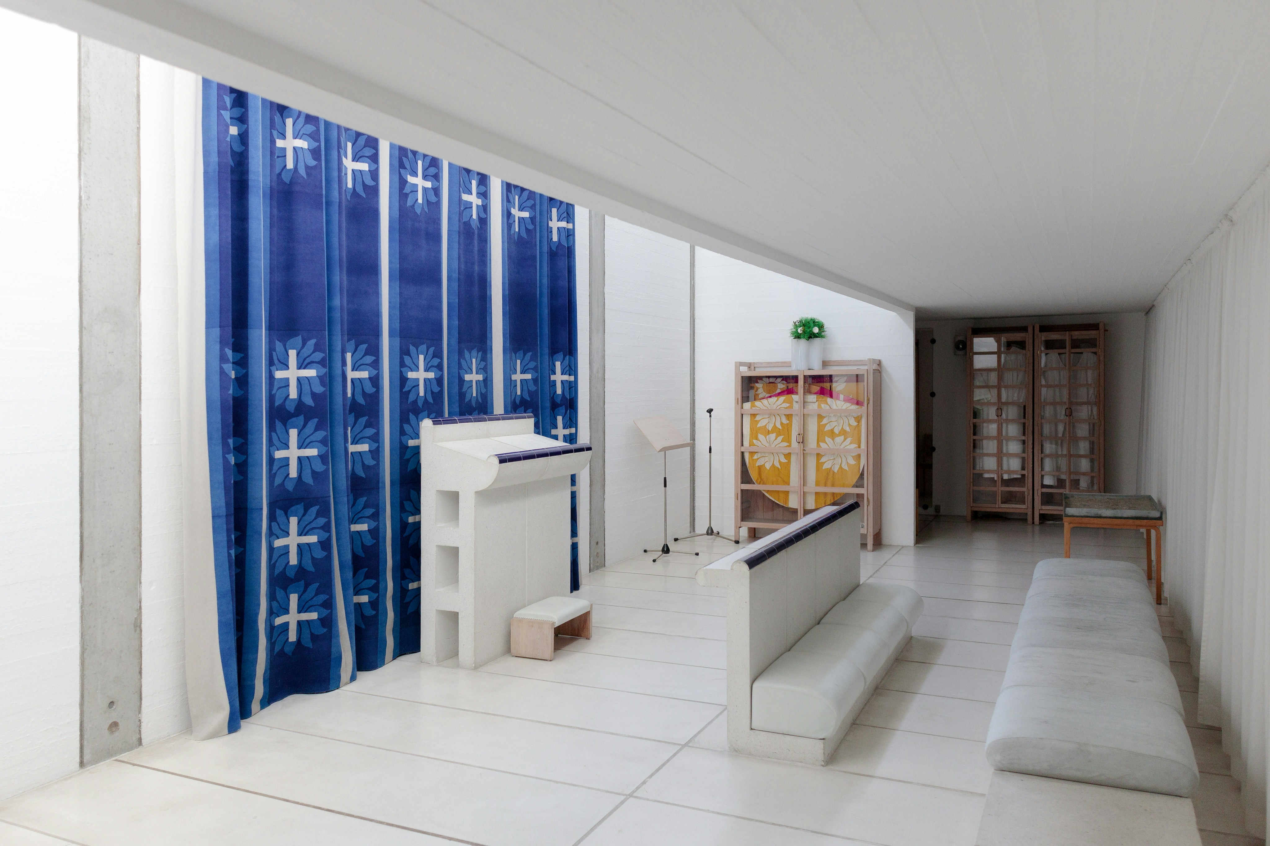 Minimalist interior featuring a blue curtain, white furnishings, and a serene atmosphere. Ideal for reflection and tranquility.