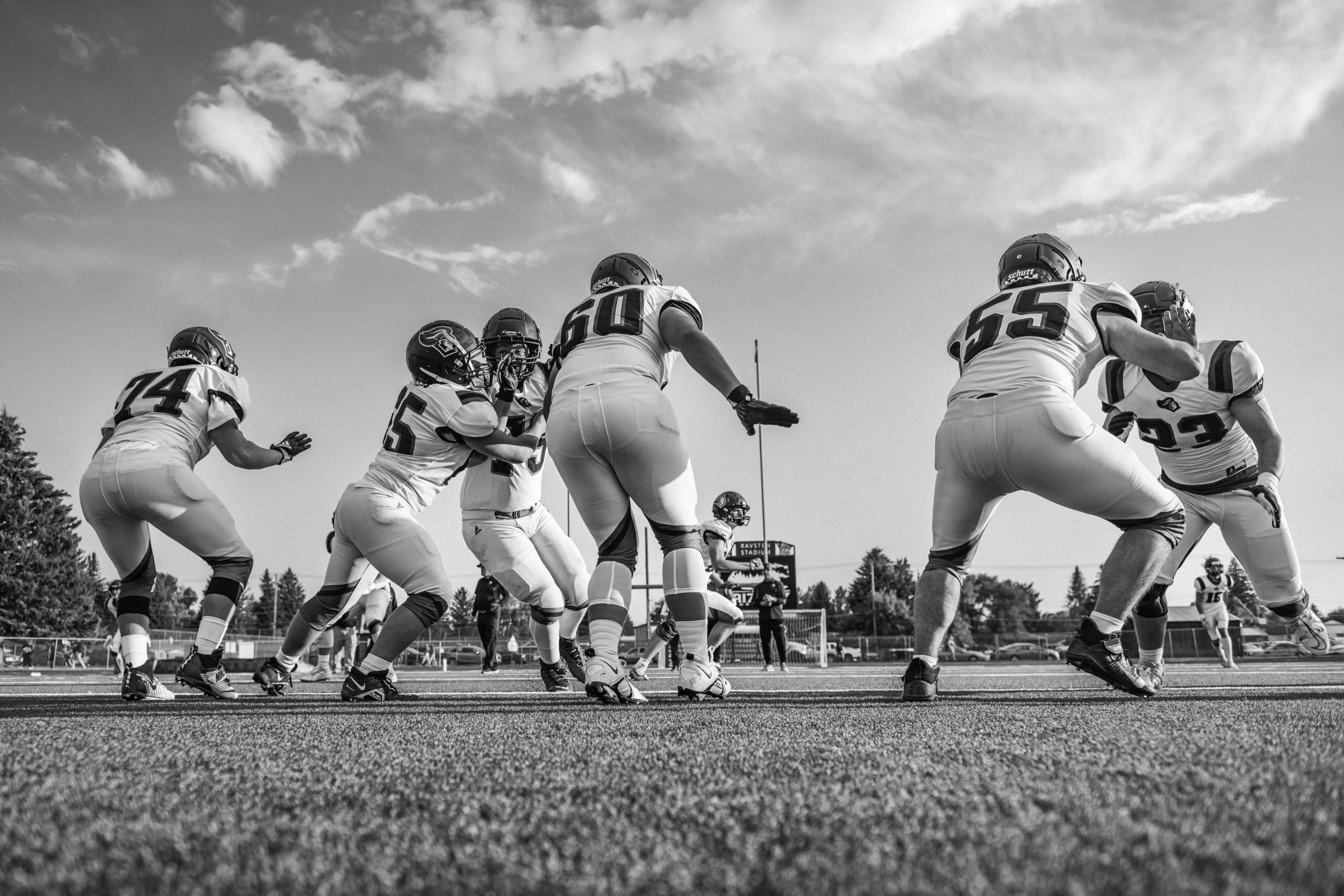 Football players in white uniforms engage in a strategic play on the field, captured in black and white. The intensity of the moment highlights teamwork and athleticism.