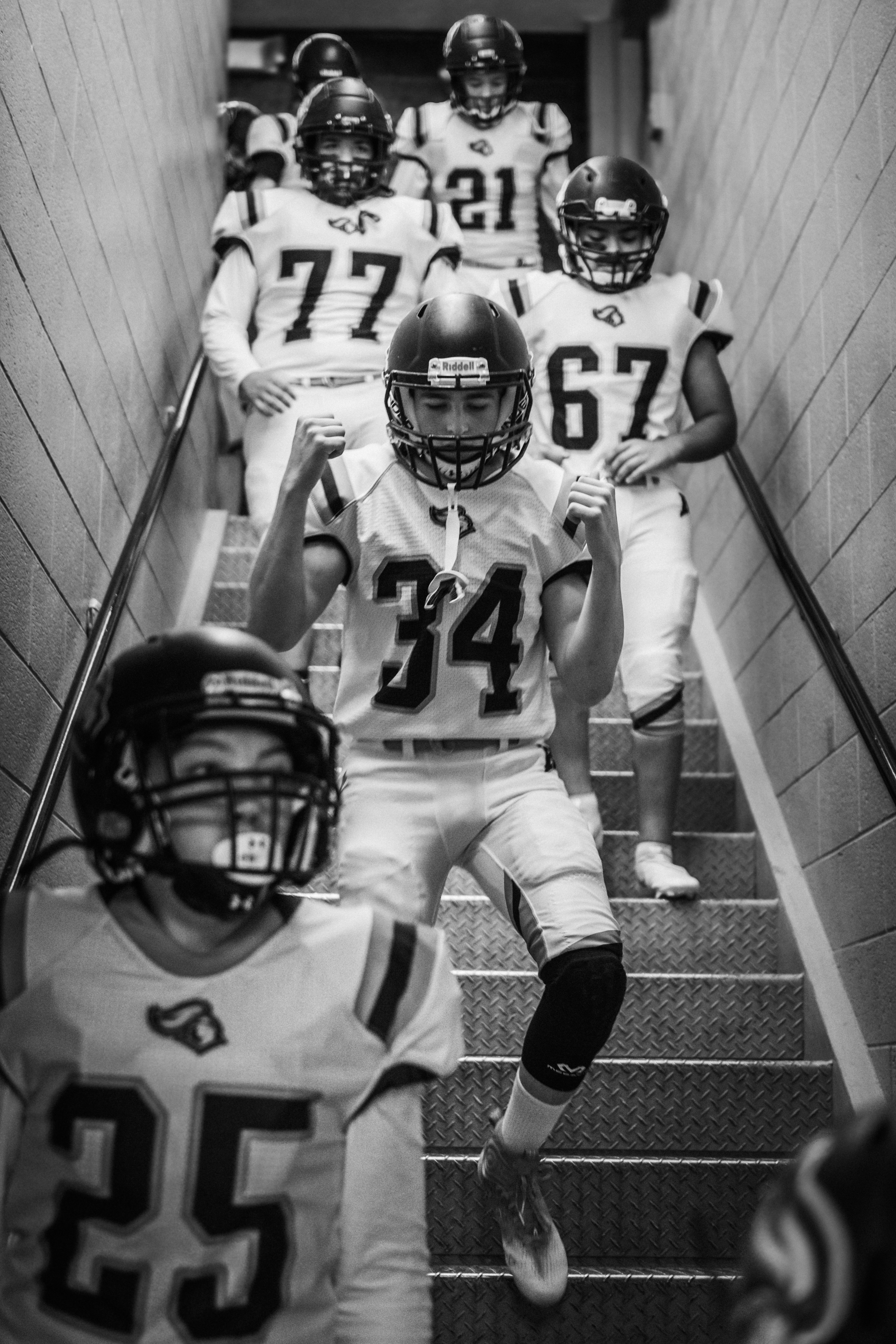 Football players ascending the stairs, showcasing their intensity and readiness for the game. The monochrome effect adds a dramatic flair to their expressions.