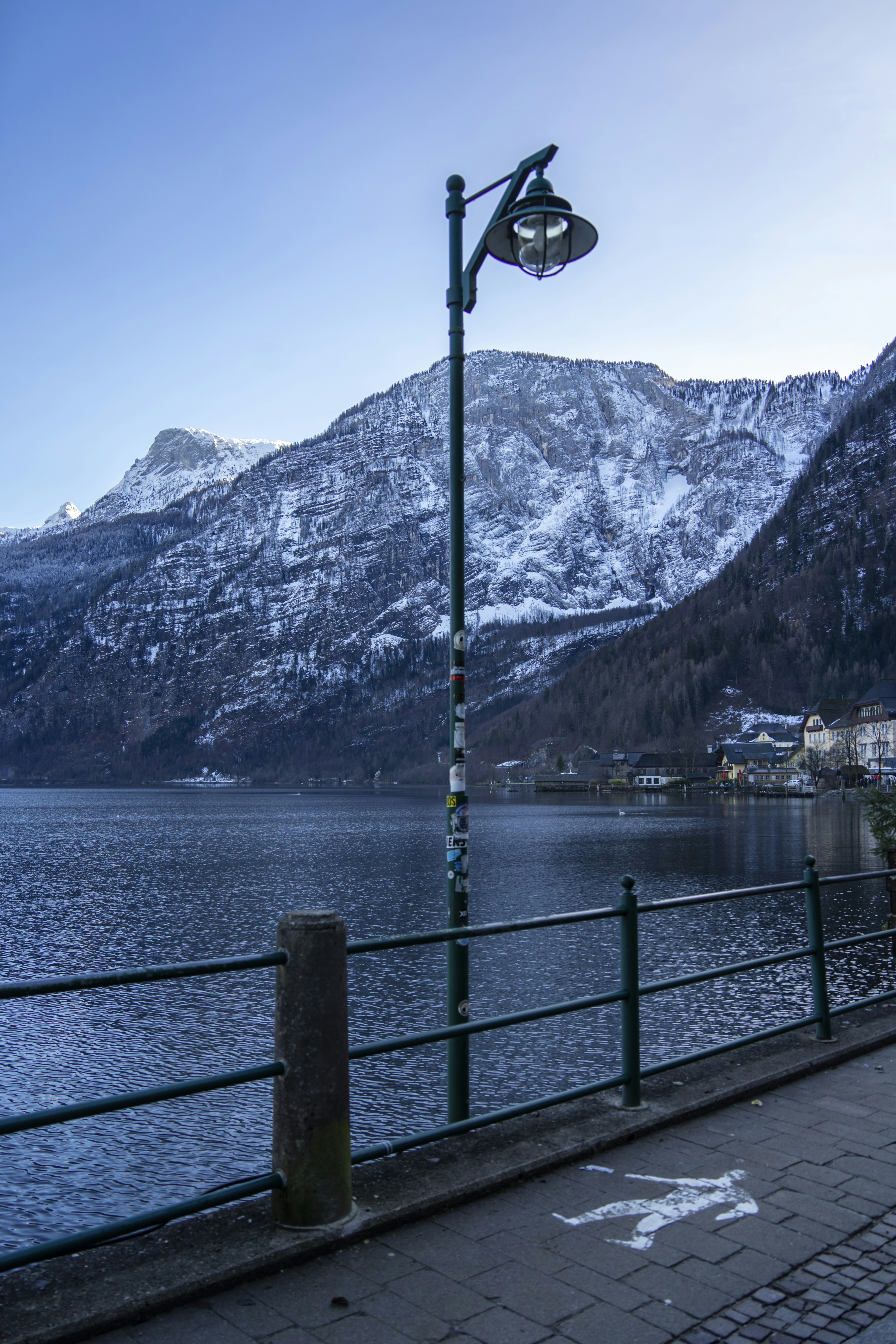 Street lamp by a lake with snow-capped mountains behind.