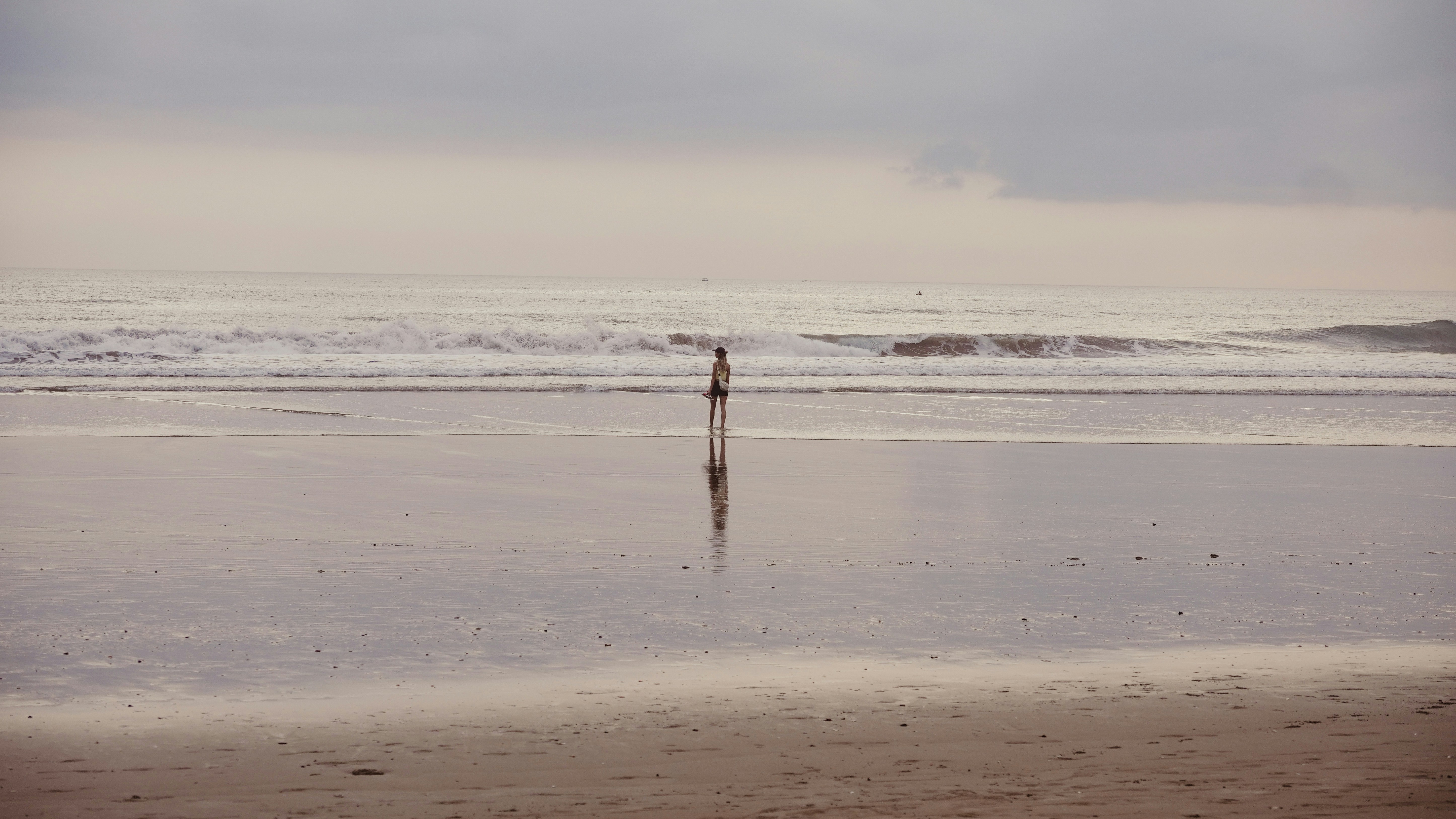 A lone figure stands on a wet sandy beach.