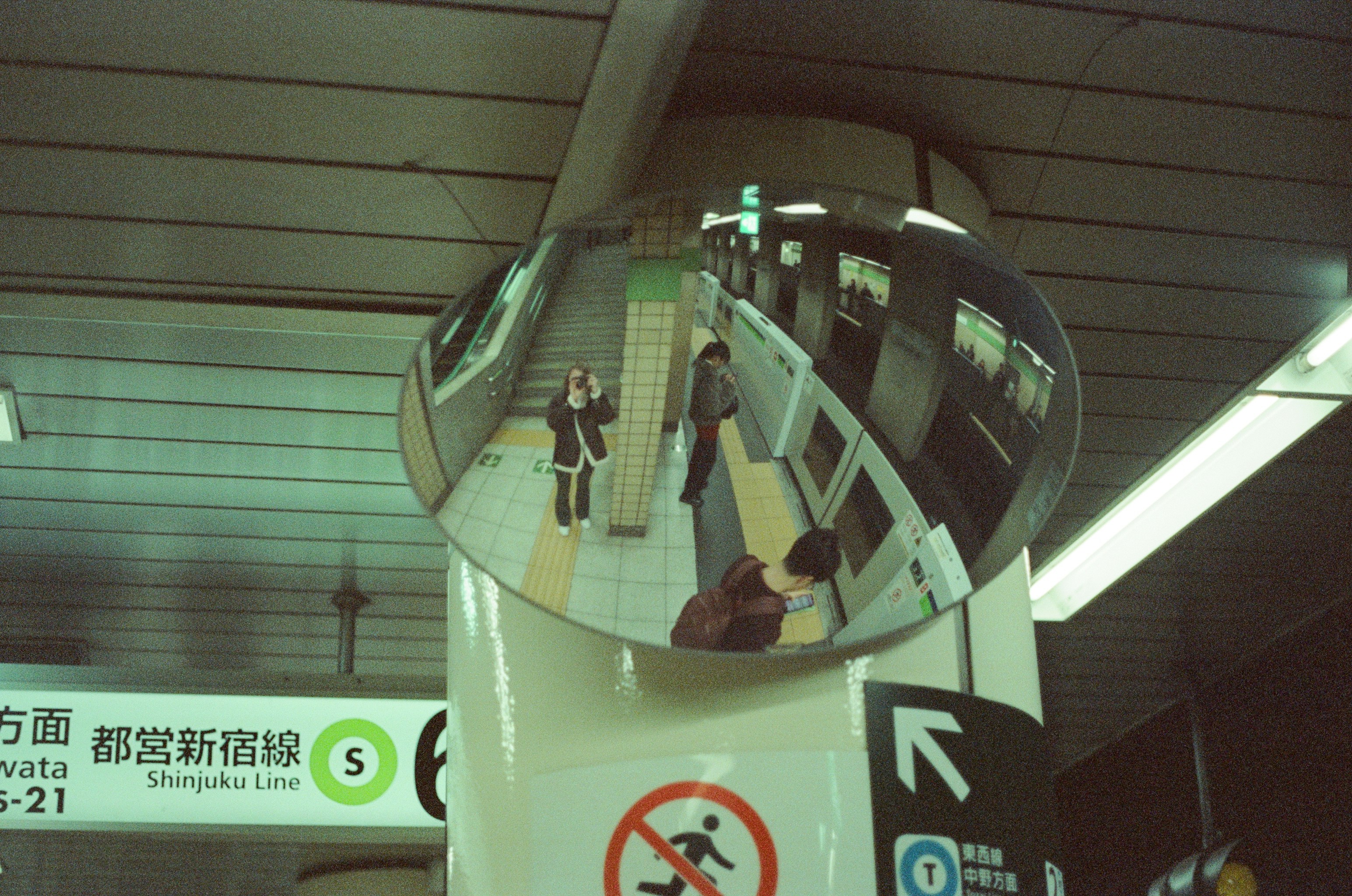 On 35mm film Kodak VISION 3 250D | People reflected in a convex mirror at a train station.