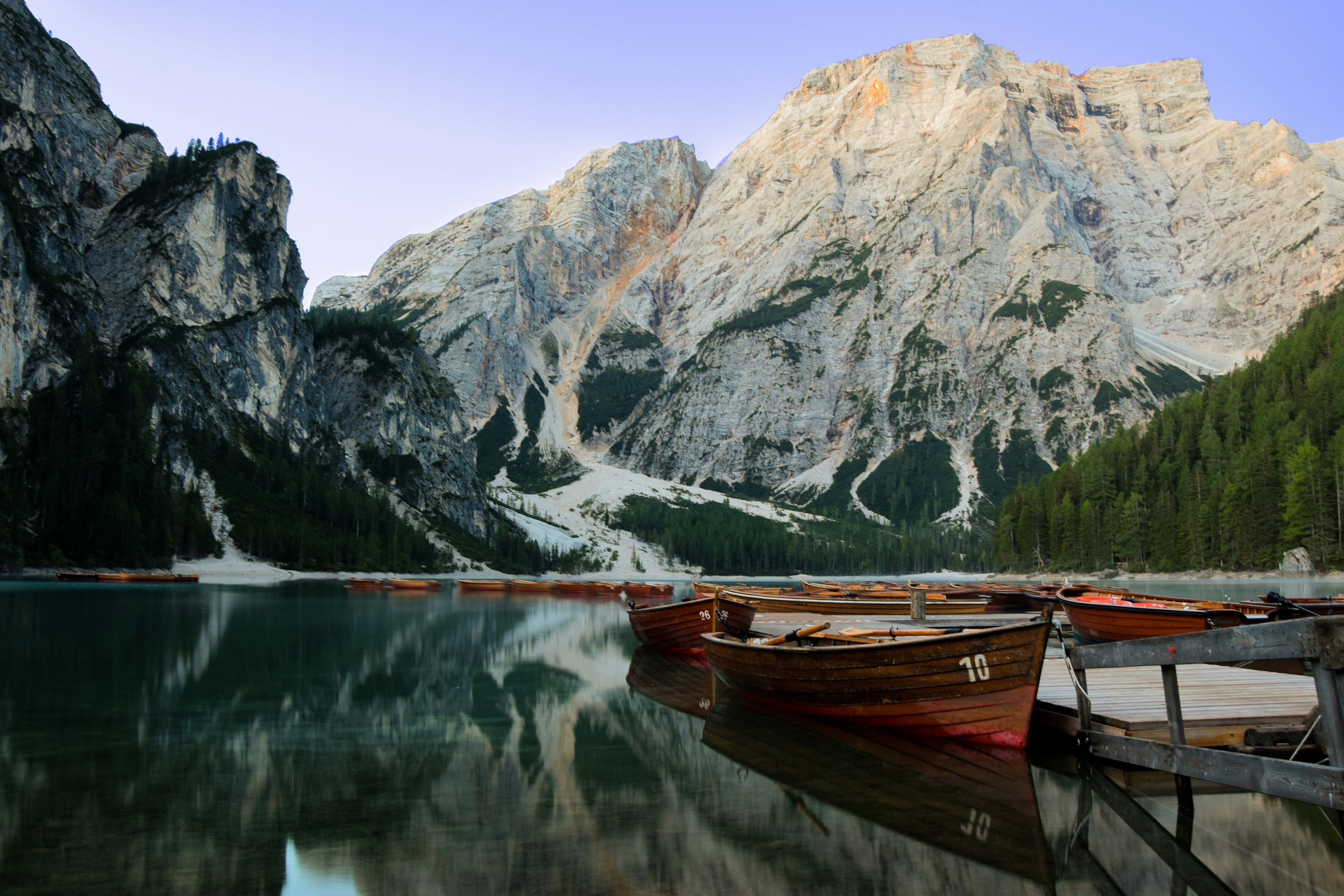 Sunrise boats | Wooden boats float on a calm lake with mountains.