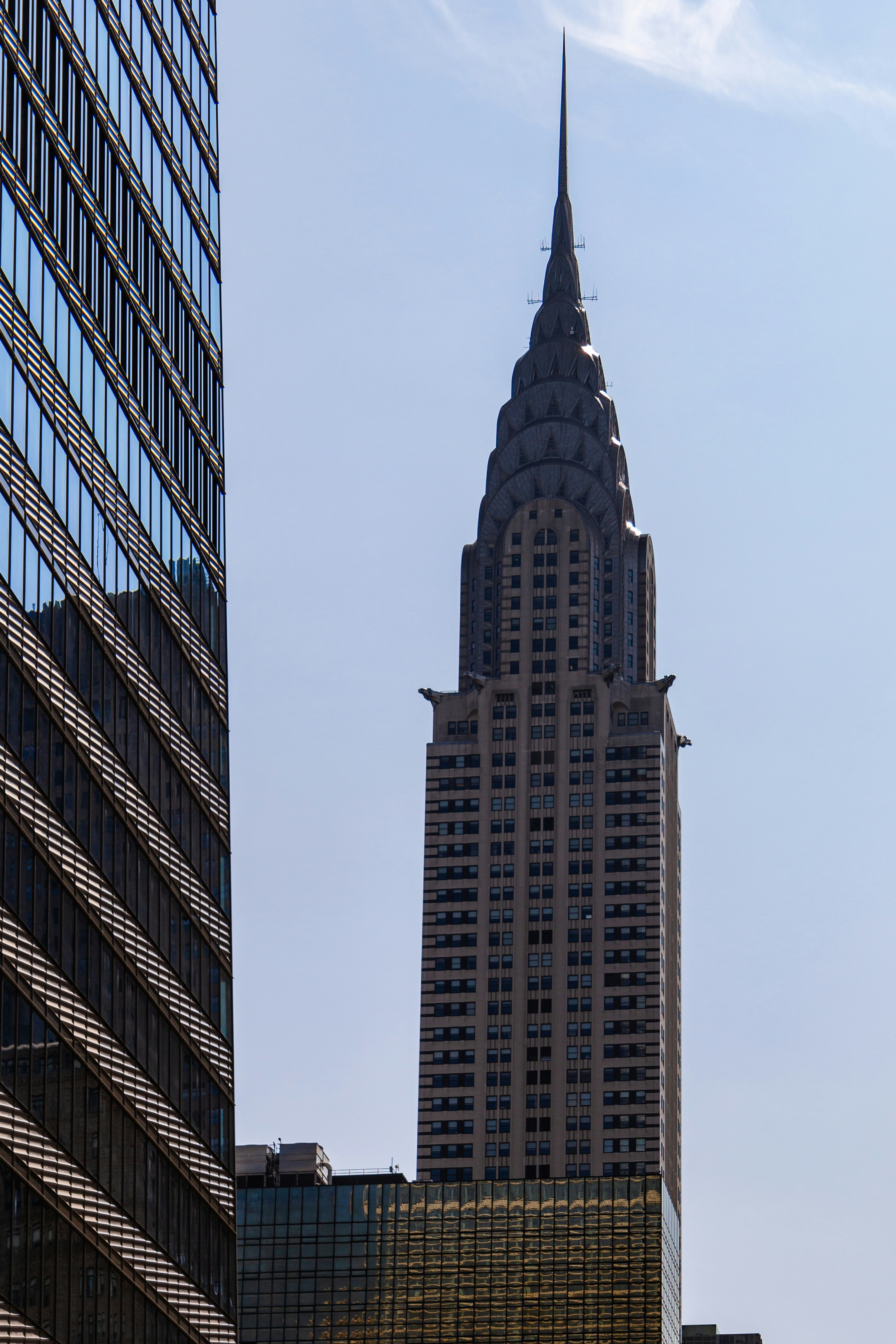 Chrysler Building reaching skyward, flanked by modern glass structures. Architectural marvel showcasing Art Deco design.