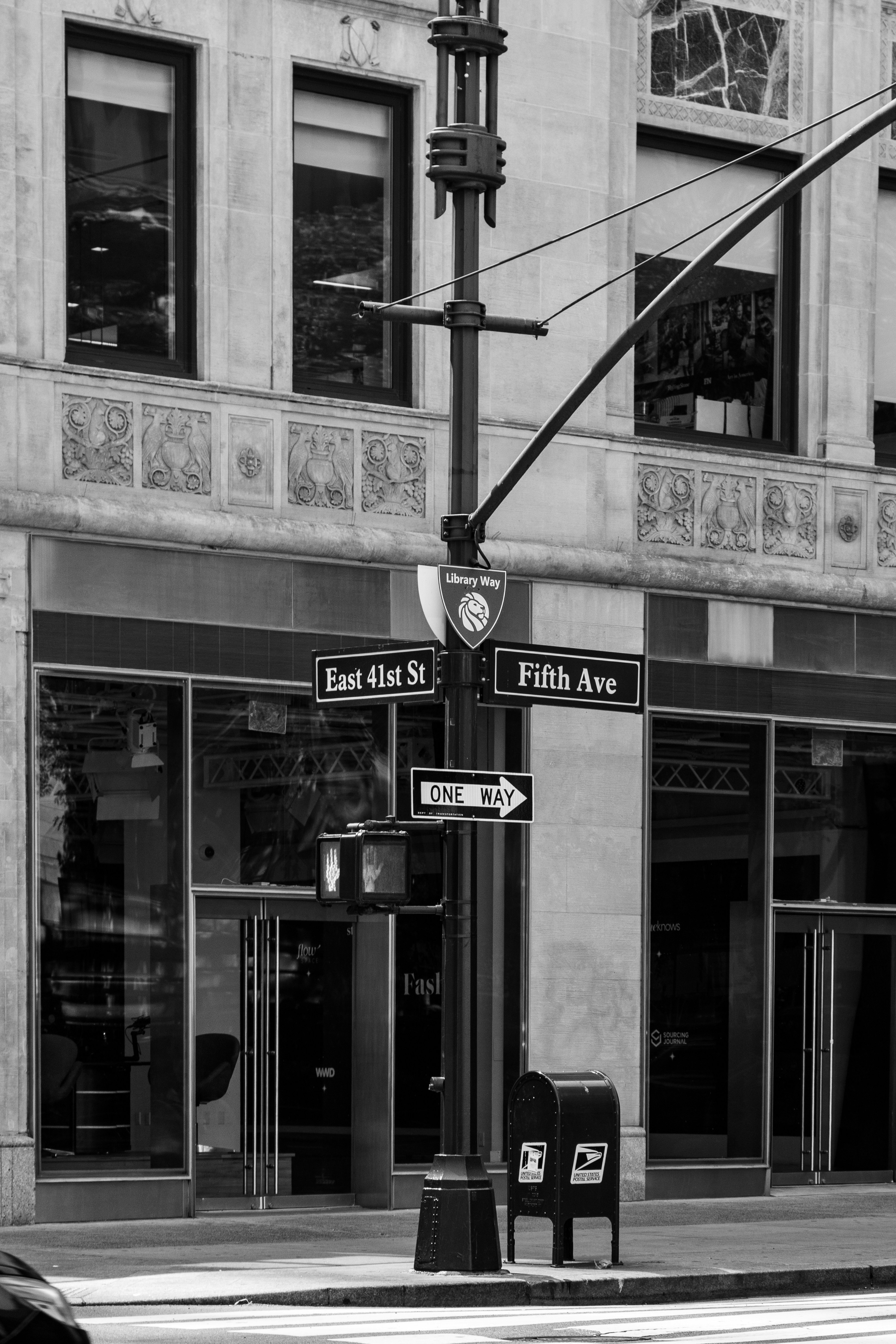 Street signs marking the intersection of East 41st St and Fifth Ave, with a backdrop of classic architecture and a black mailbox. 