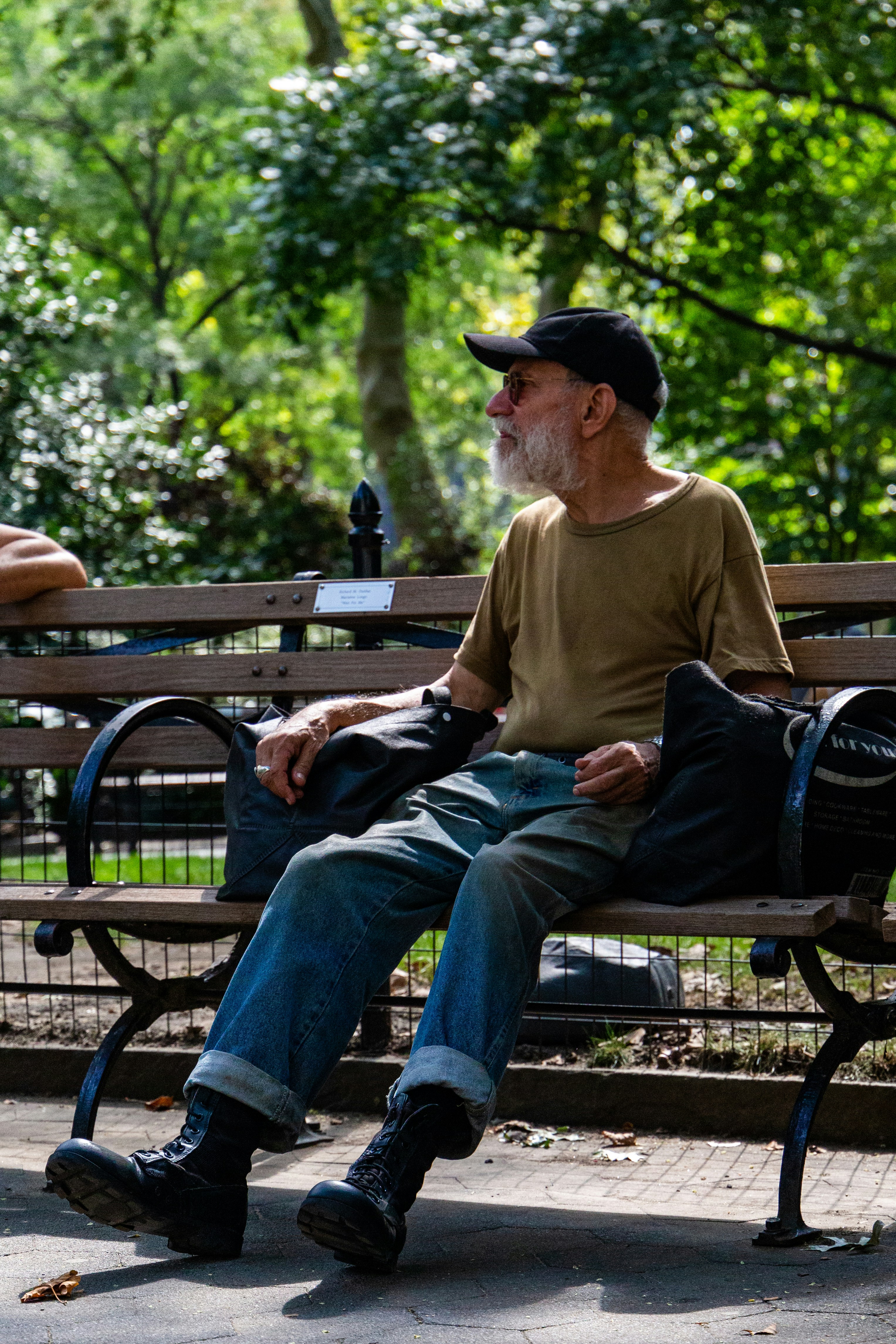 Elderly man sitting on a park bench, gazing thoughtfully into the distance, surrounded by lush greenery.