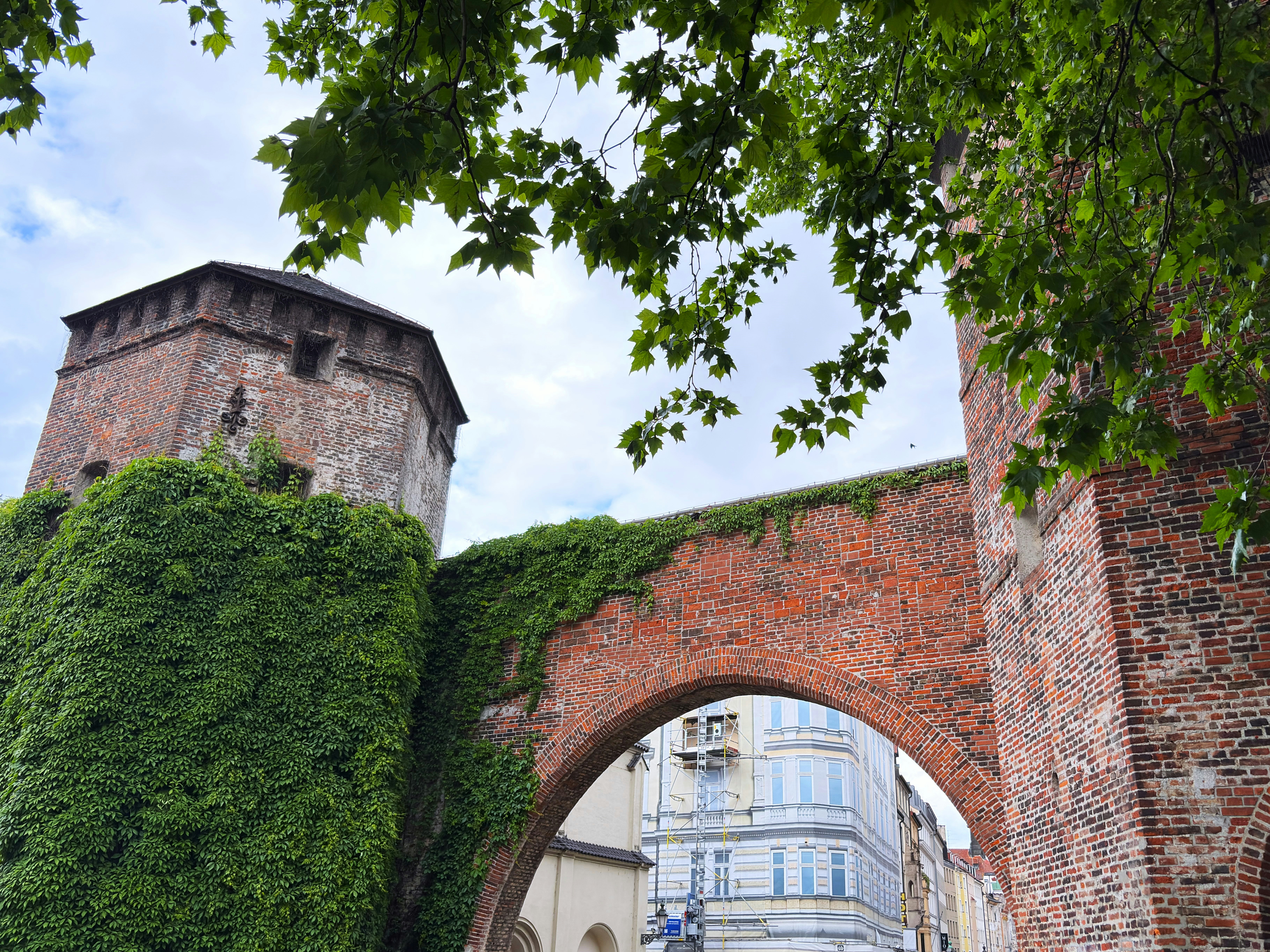 The Sendlinger Tor, one of the three remaining medieval city gates in Munich, Germany. | Historic brick archway covered in green ivy