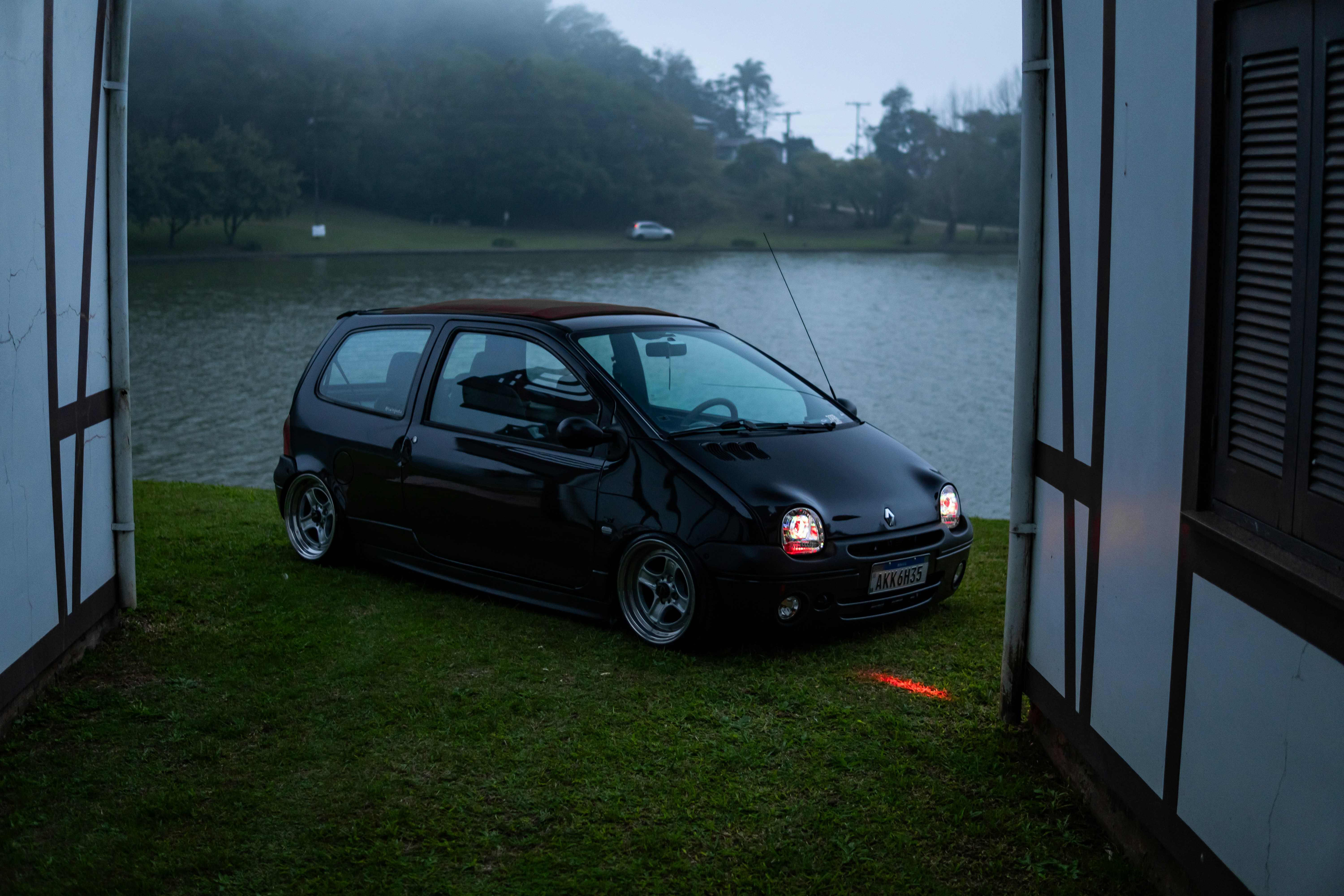 Low-Slung Hatchback by the Lake: A Moody Dusk Portrait Between White-Framed Sheds