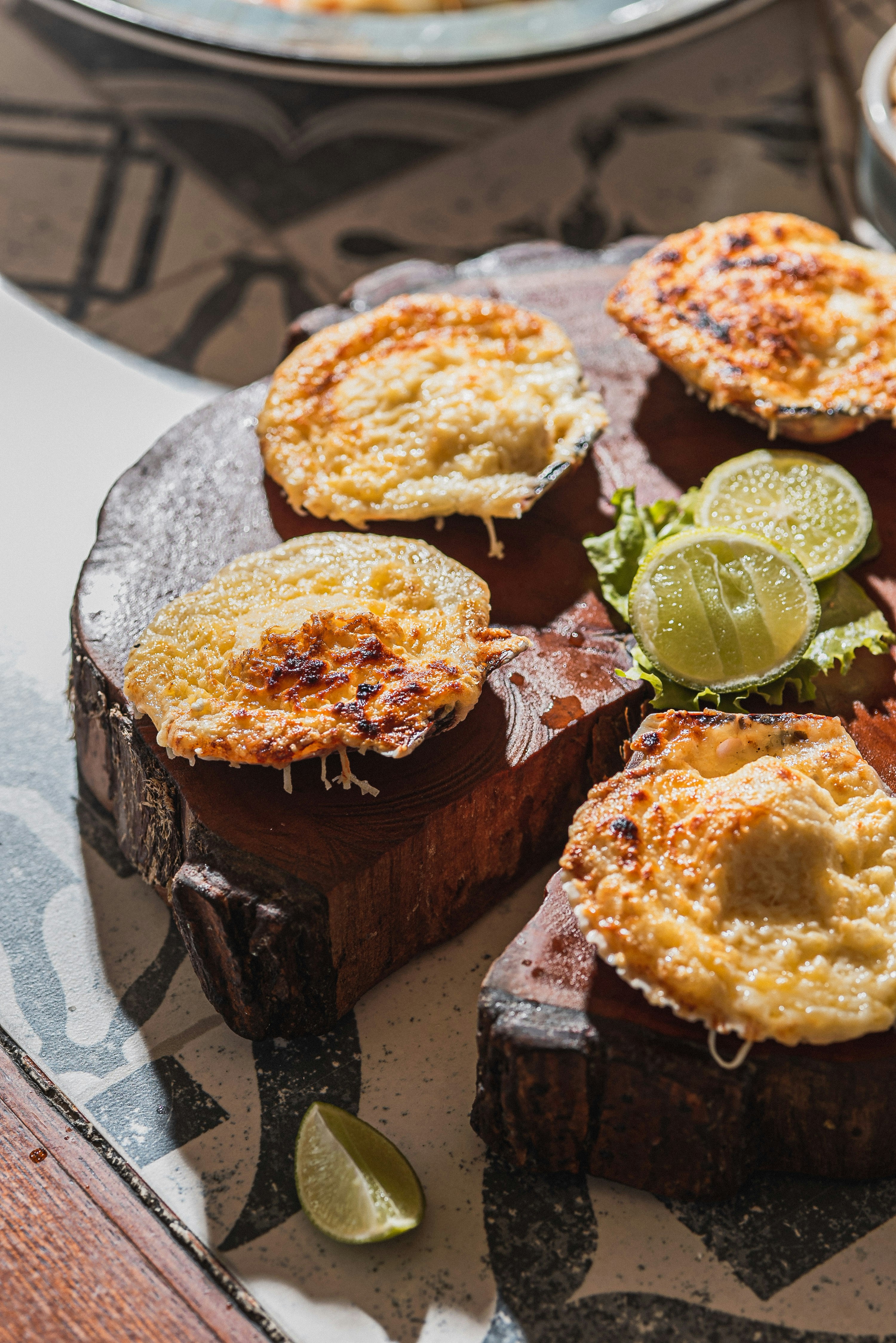 Crostini on charred wood: melted cheese crowns with lime accents in warm daylight